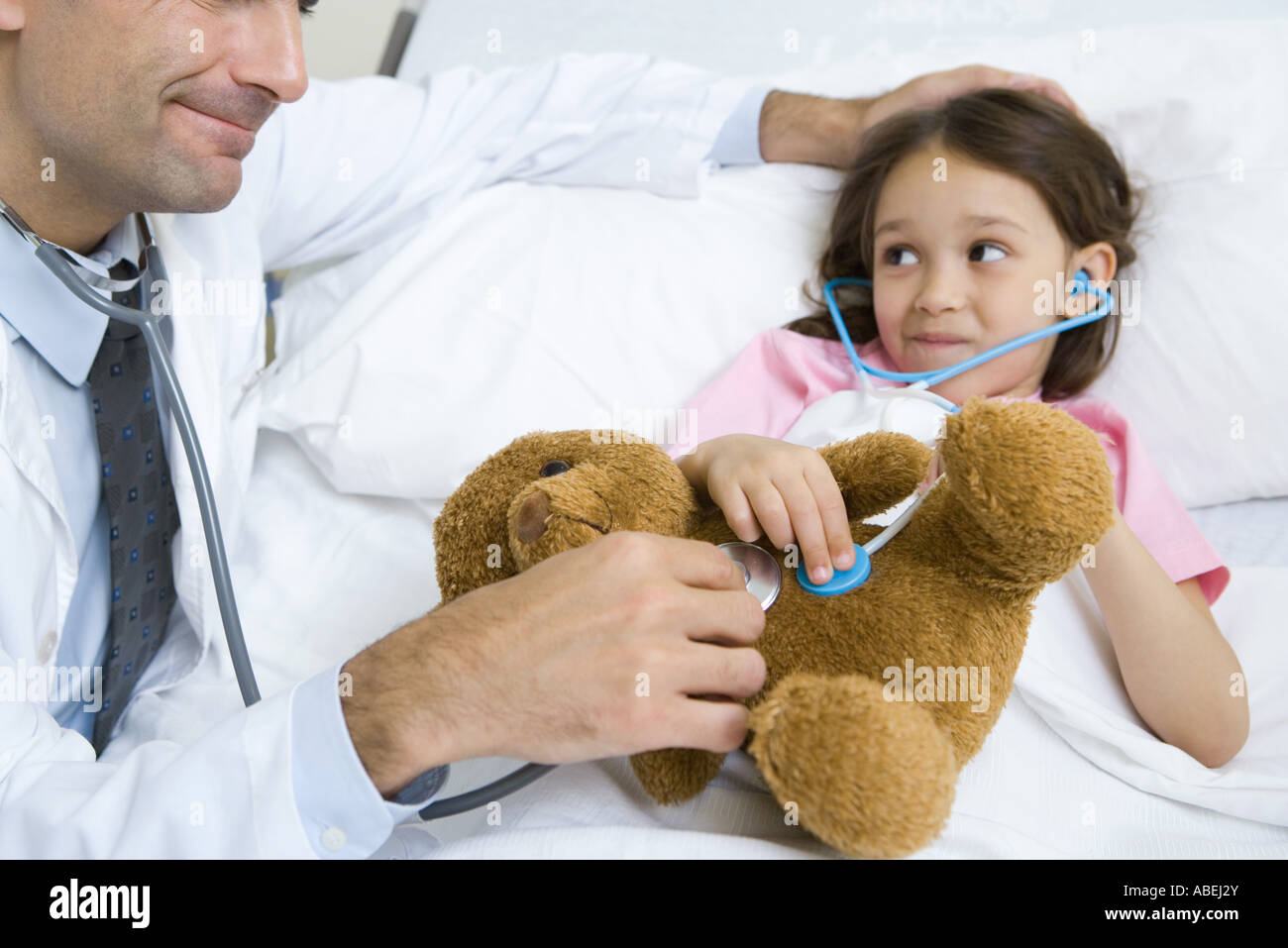 Girl lying in hospital bed, smiling at doctor as both hold stethoscopes ...