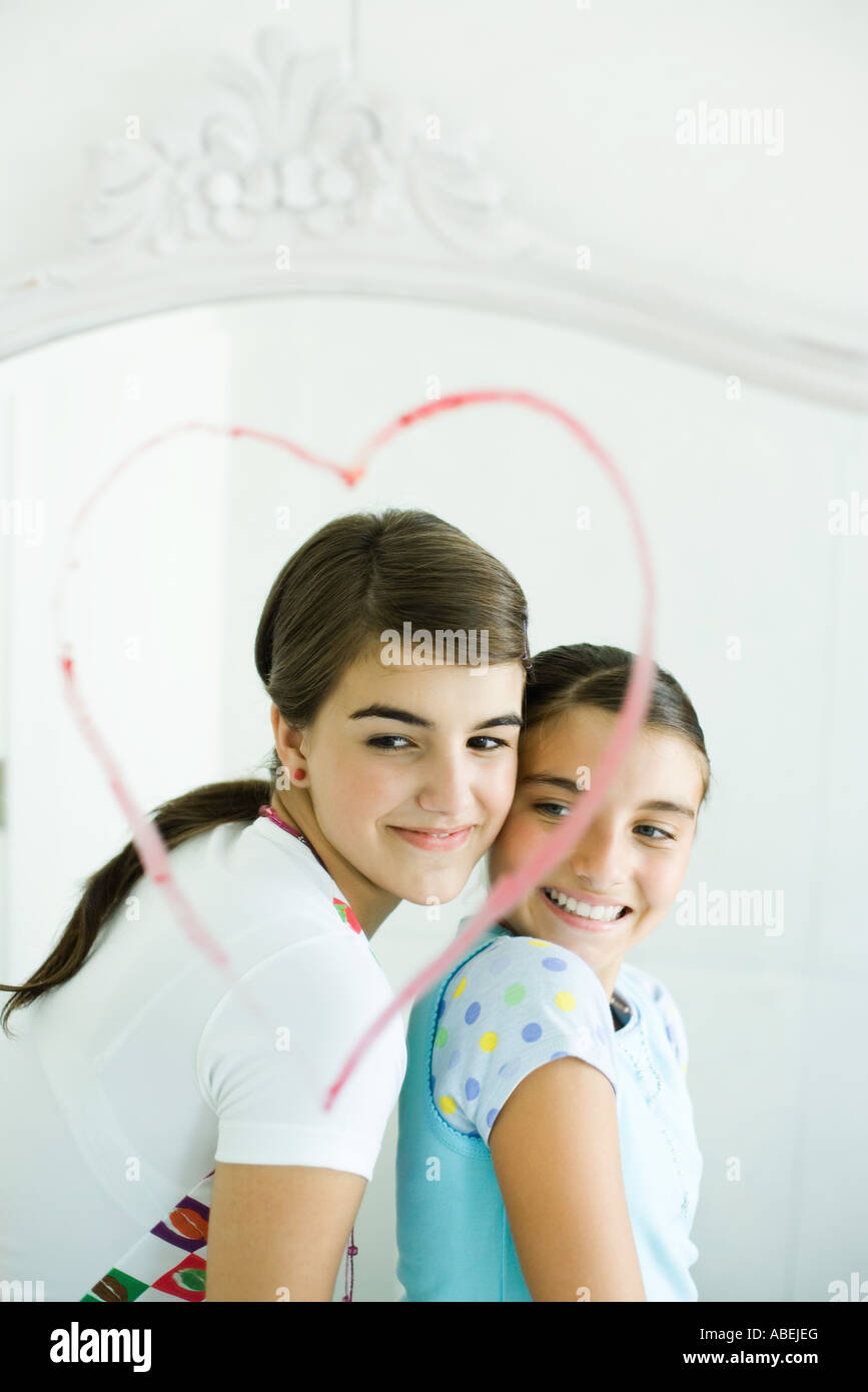 Two young female friends, reflected in mirror with heart drawn in ...