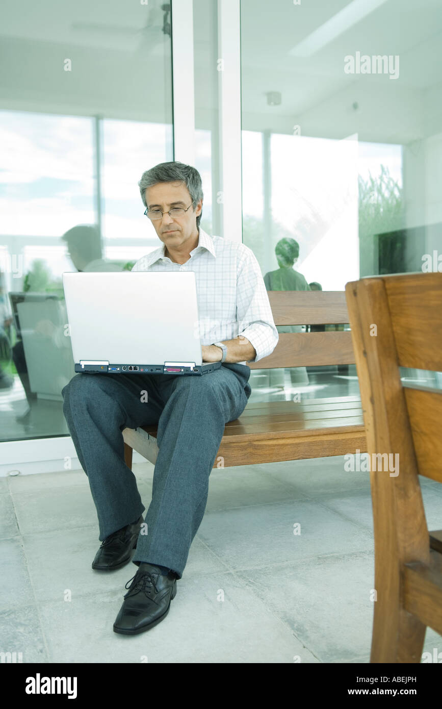 Man sitting, using laptop on patio, full length Stock Photo - Alamy