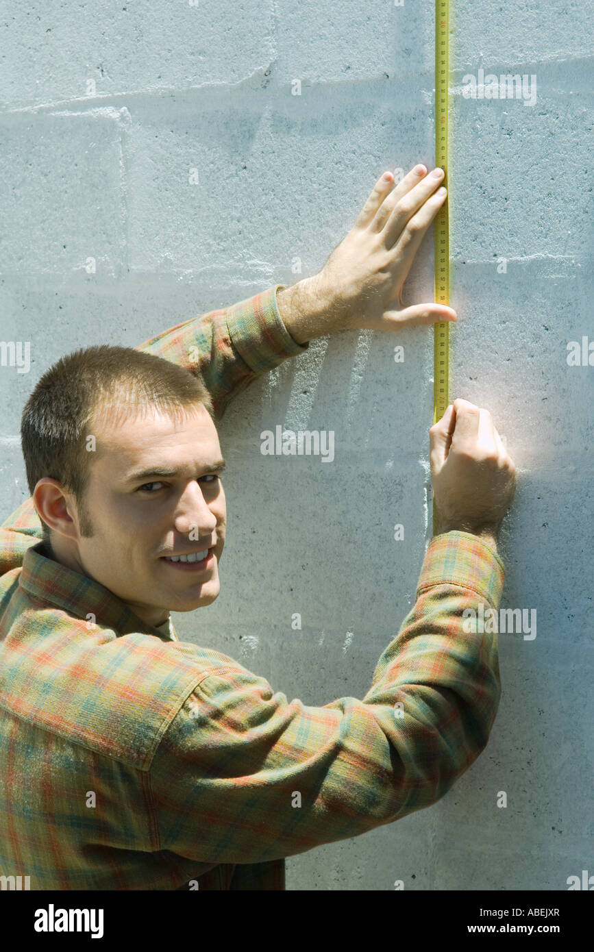 Man measuring wall with measuring tape, smiling over shoulder at camera ...
