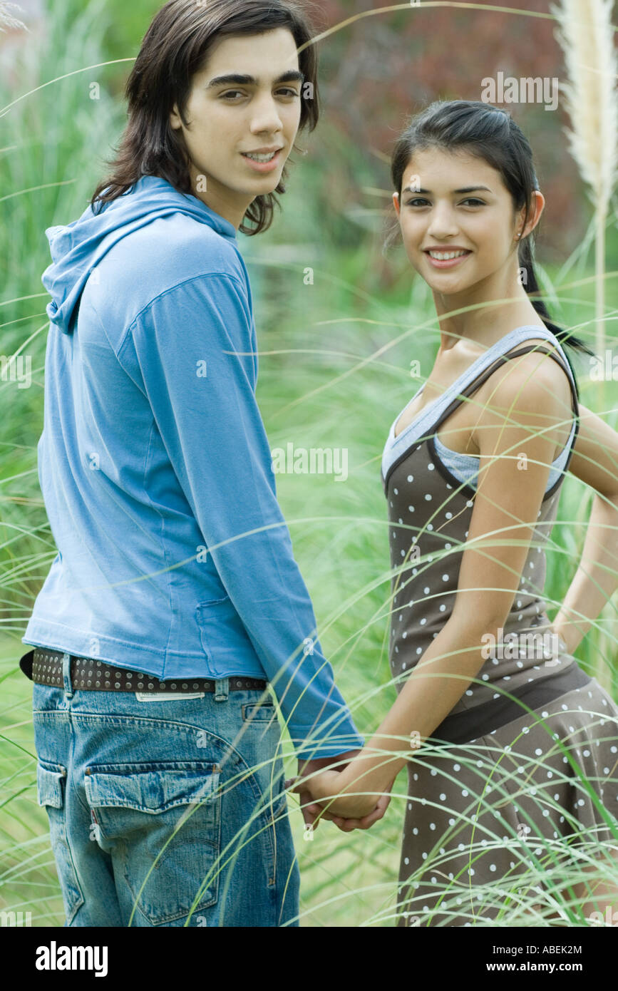 Young couple holding hands, looking over shoulders at camera Stock ...