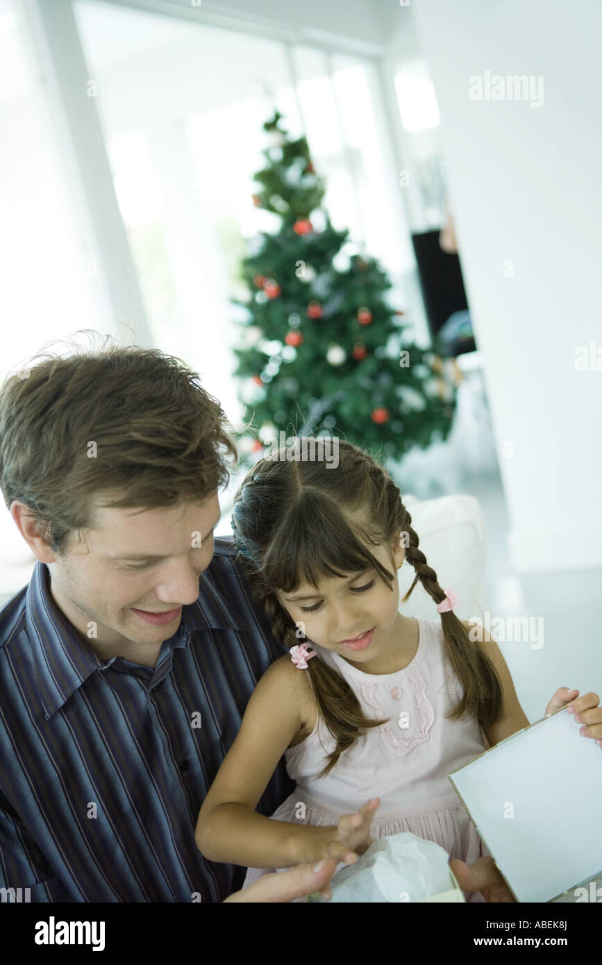 Girl sitting on father's lap, opening Christmas present Stock Photo - Alamy