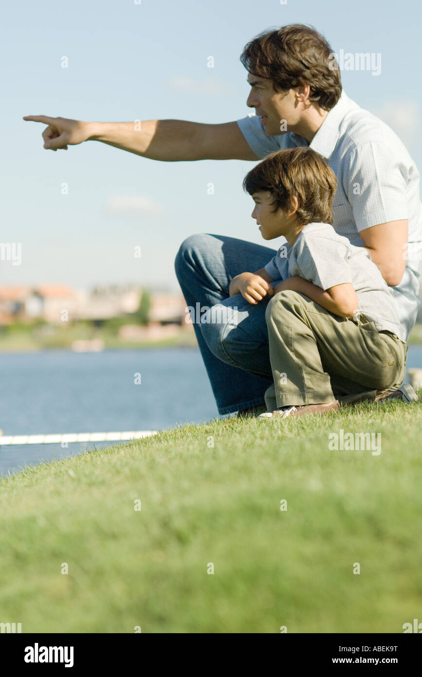 Father and son sitting by edge of water, looking toward distance Stock ...