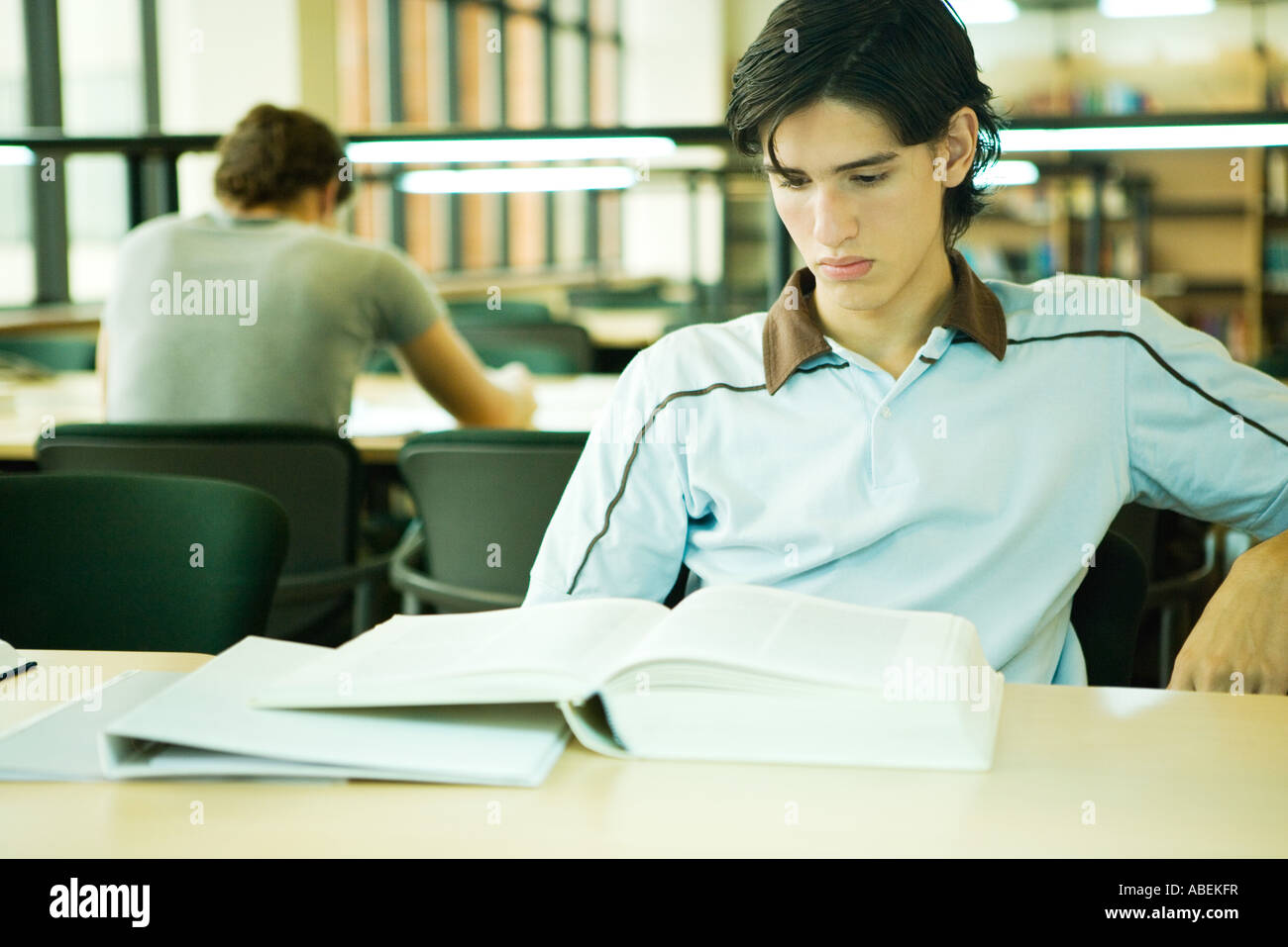 Close up of boy sitting in library reading book hi-res stock ...