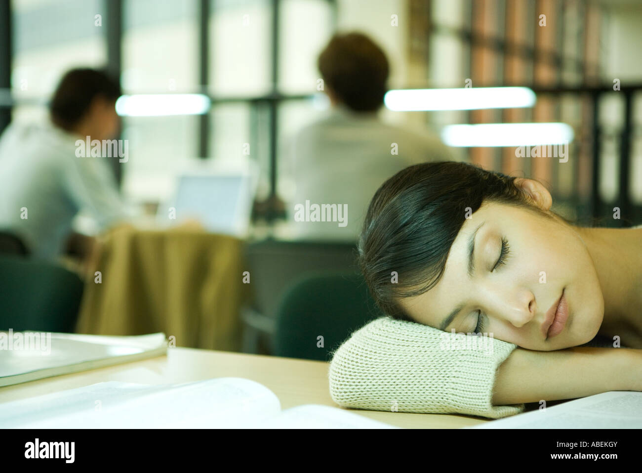 Female college student sitting at table in library, resting head on ...