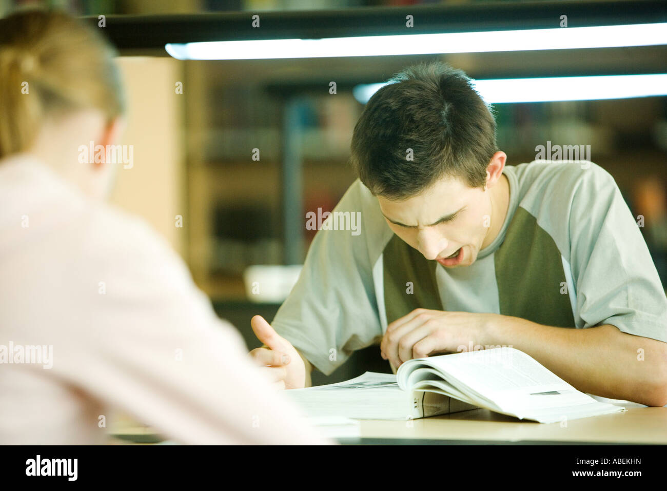 Male college student sitting in library, studying and yawning Stock ...