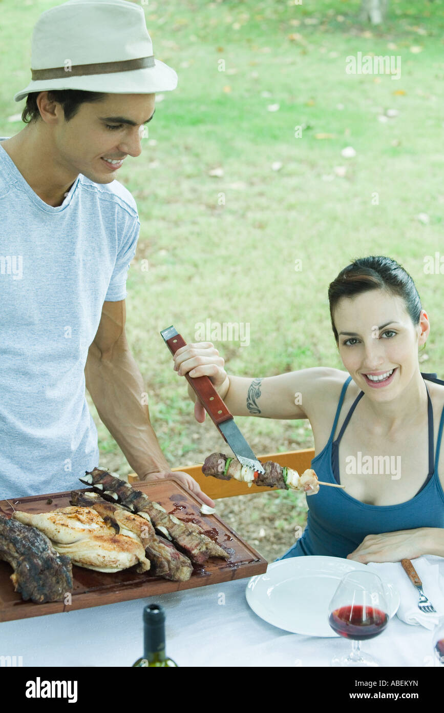 Woman taking kebab from tray of grilled meats, smiling at camera Stock ...