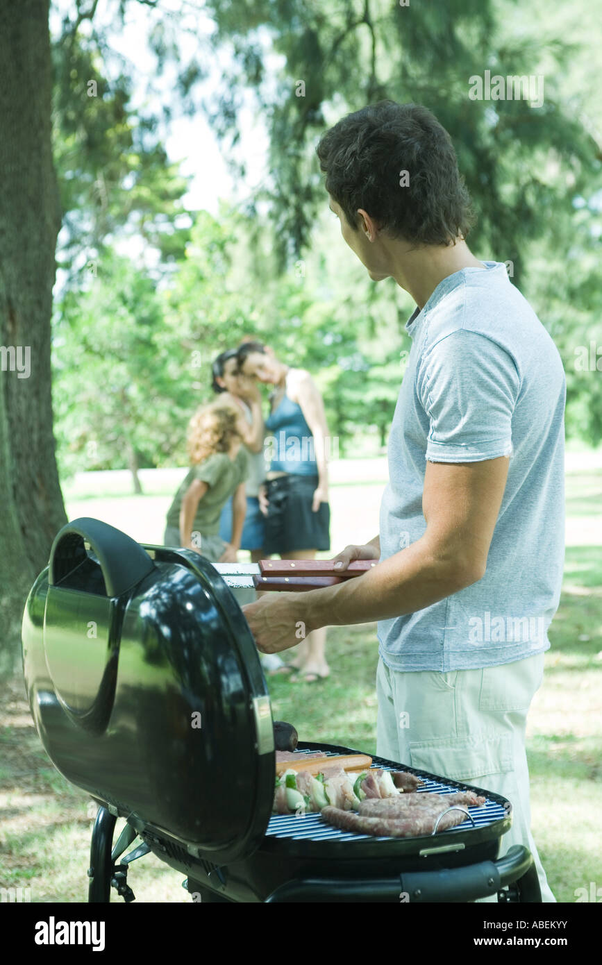 Man grilling meat on barbecue, family whispering in background Stock ...