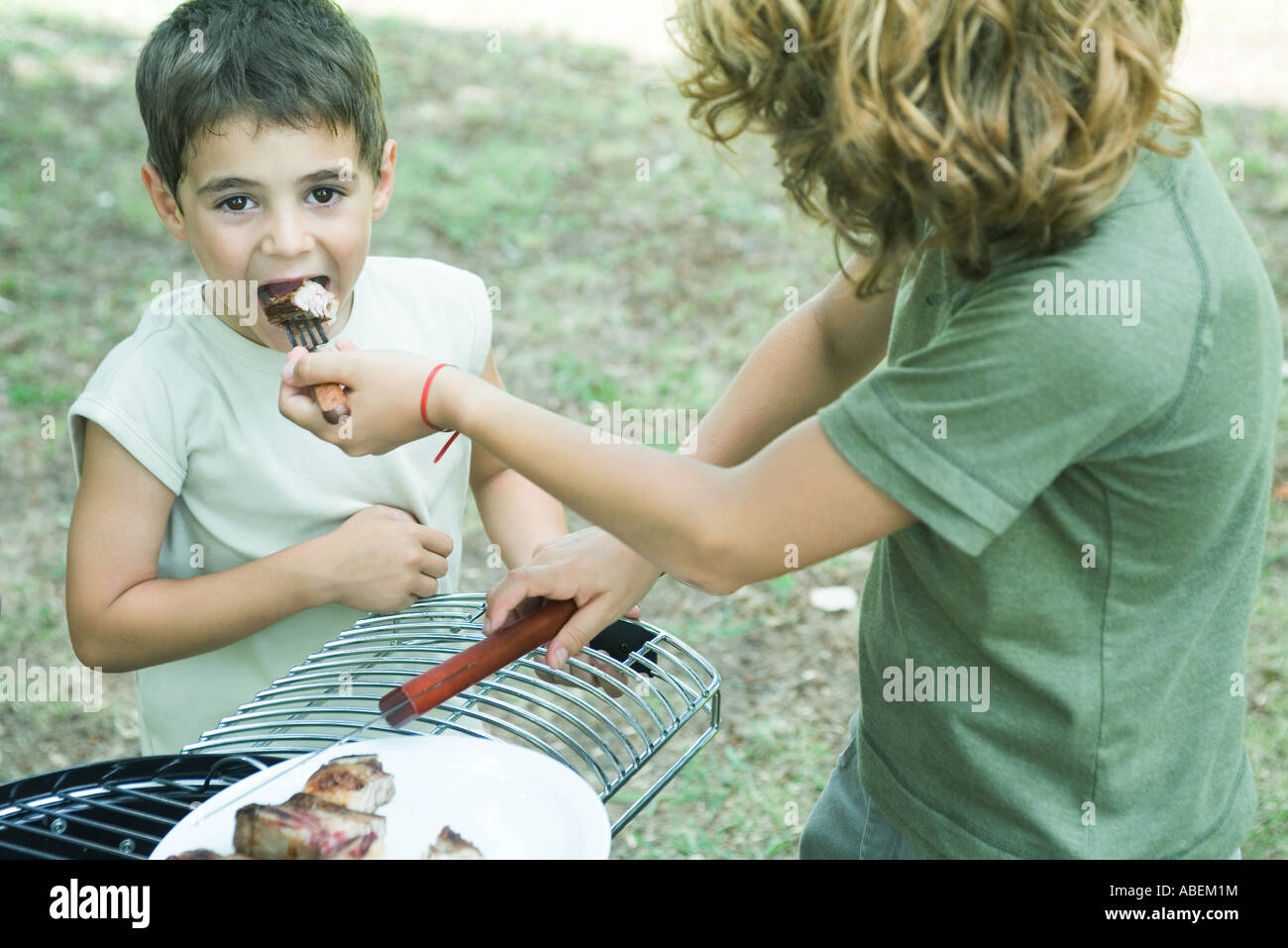 Boy feeding bite of grilled meat to younger boy Stock Photo - Alamy