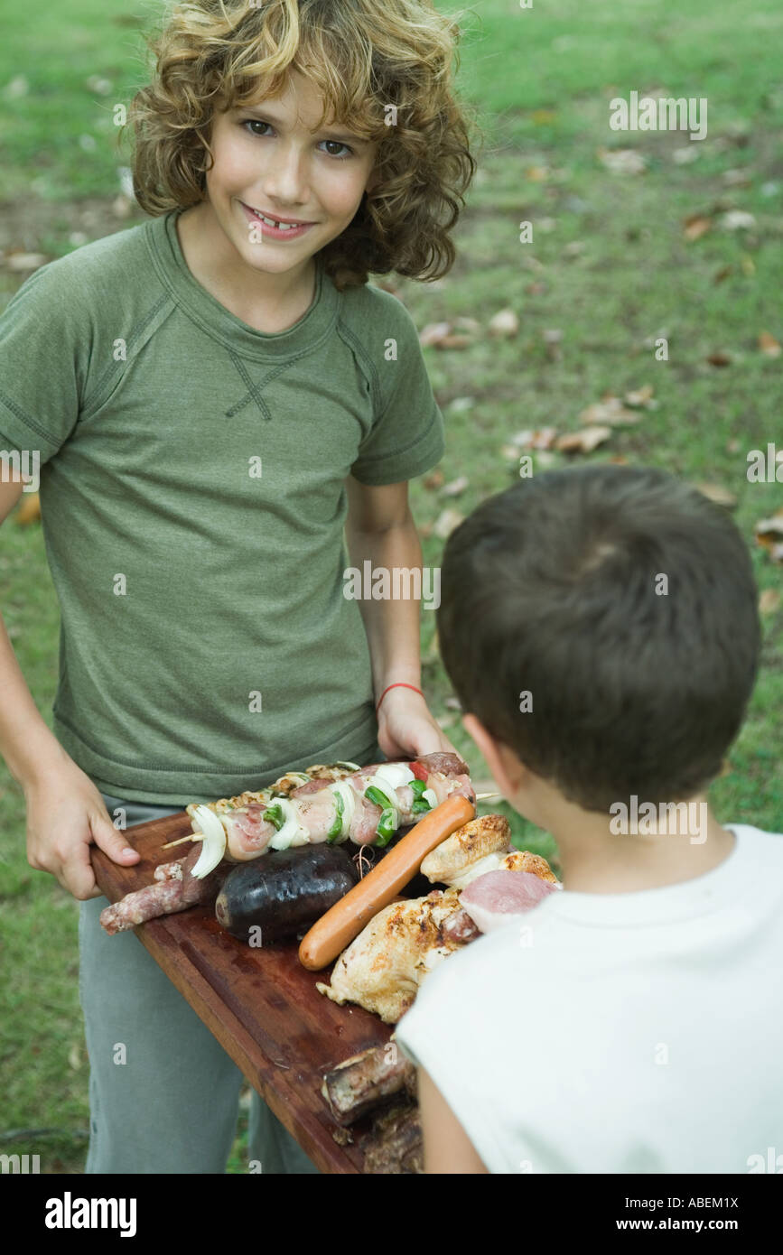 Two boys carrying tray of grilled meat Stock Photo - Alamy