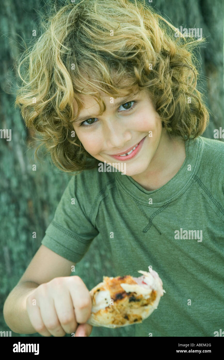 Boy holding grilled chicken leg, smiling at camera, portrait Stock ...