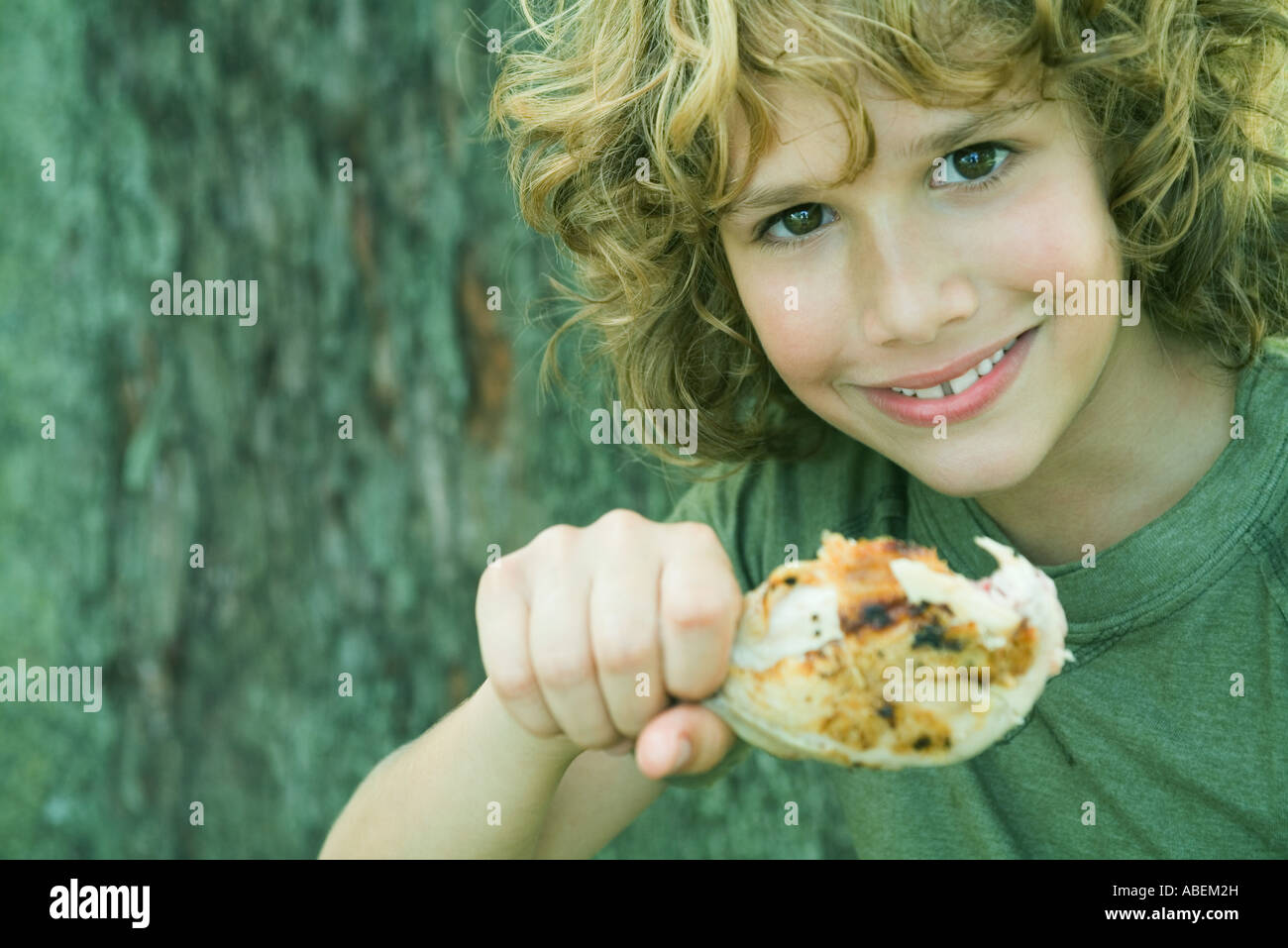 Boy holding grilled chicken leg, smiling at camera, portrait Stock ...