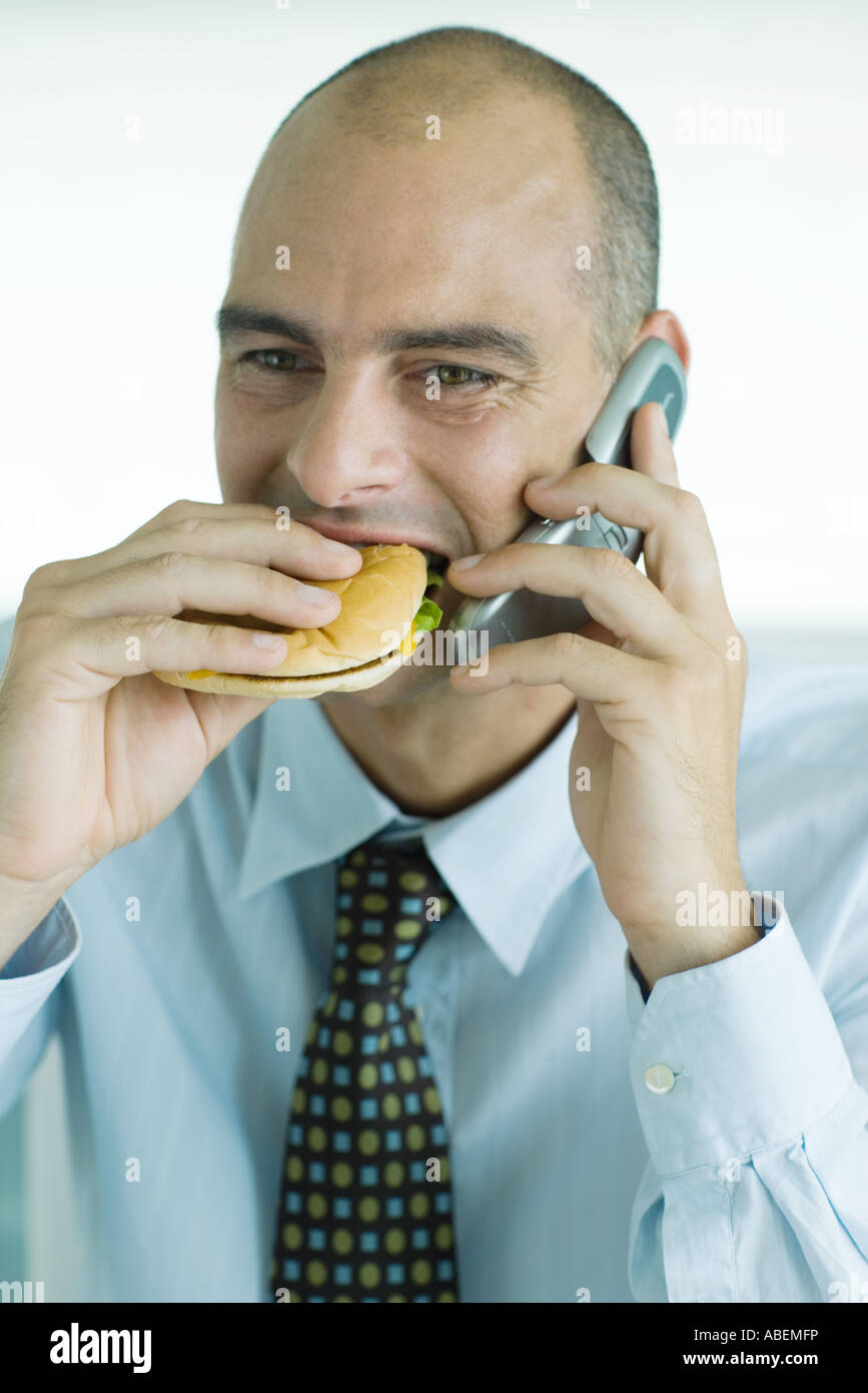 Man eating hamburger and using cell phone Stock Photo - Alamy