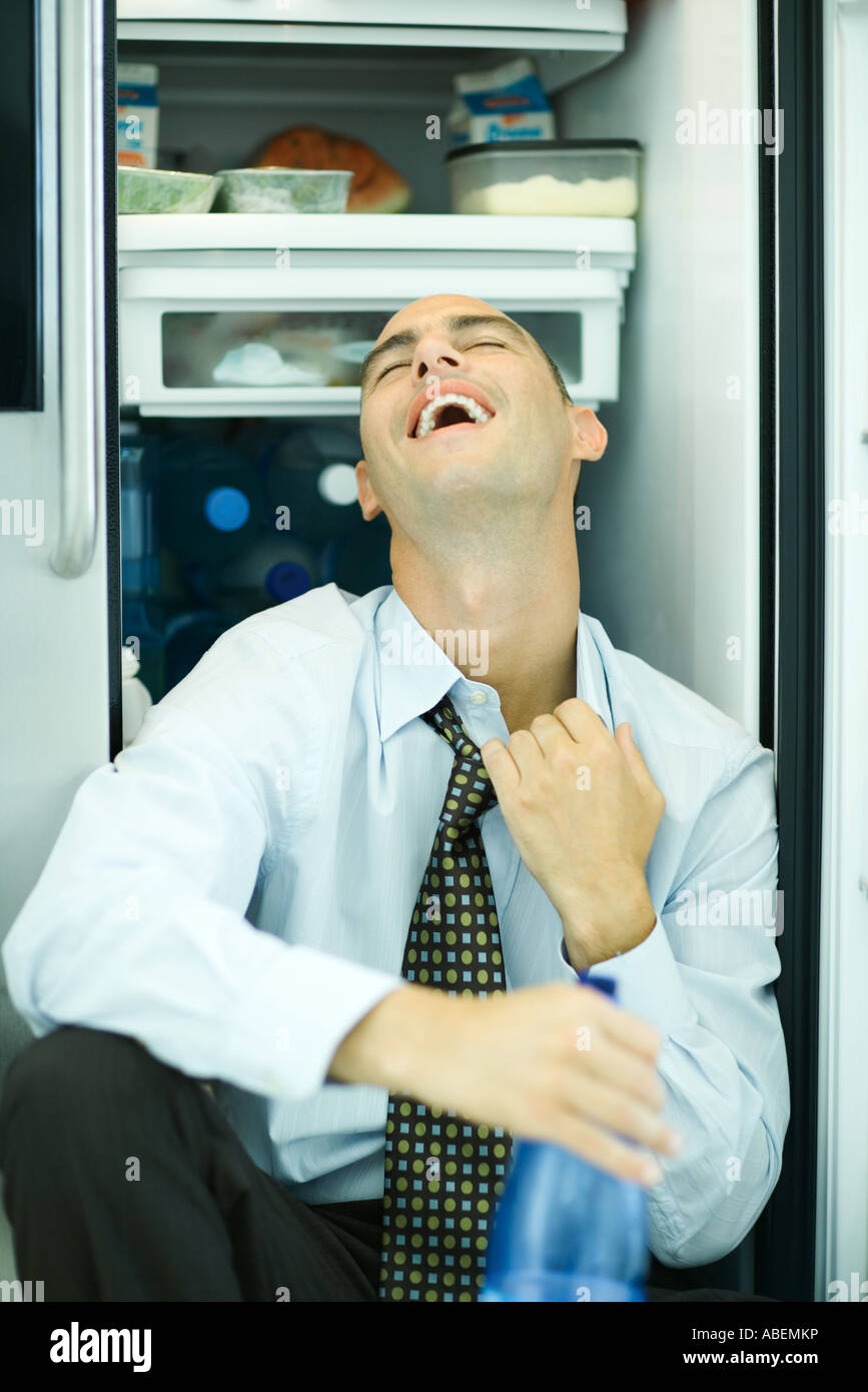 Man sitting in front of open refrigerator, pulling on collar, head back ...