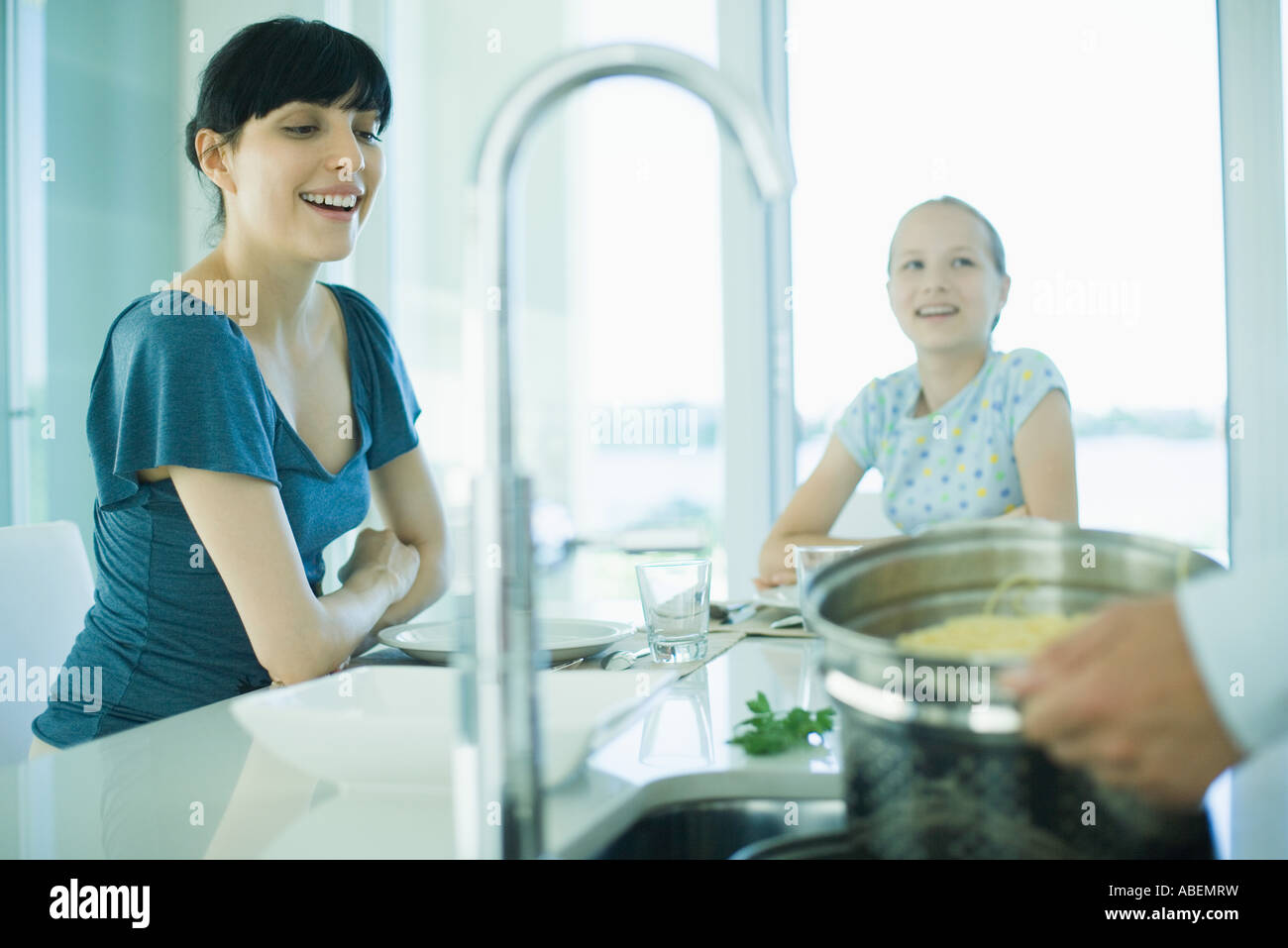Man draining spaghetti over kitchen sink while wife and daughter watch ...