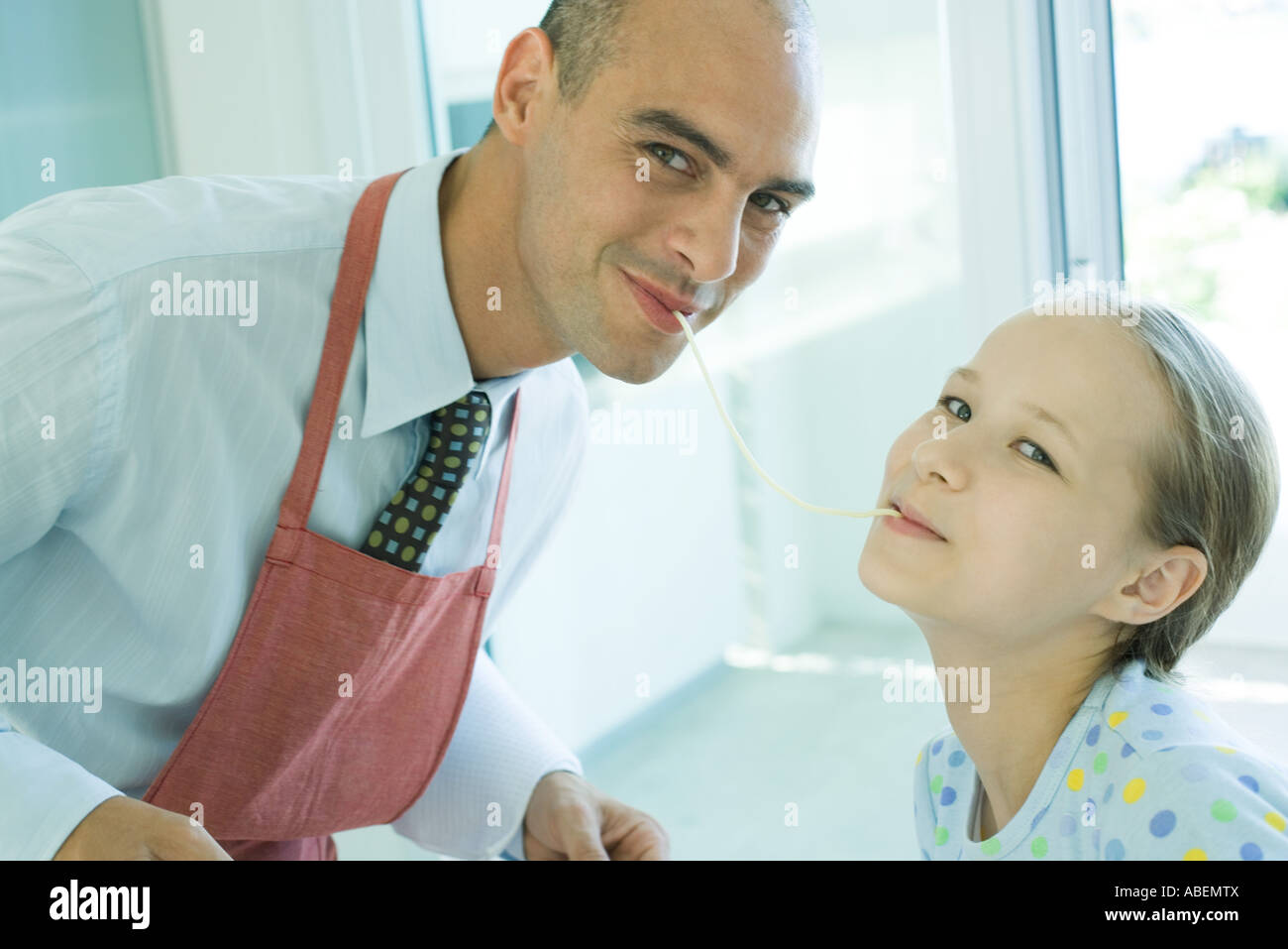 Father and daughter sharing spaghetti noodle, smiling at camera Stock ...