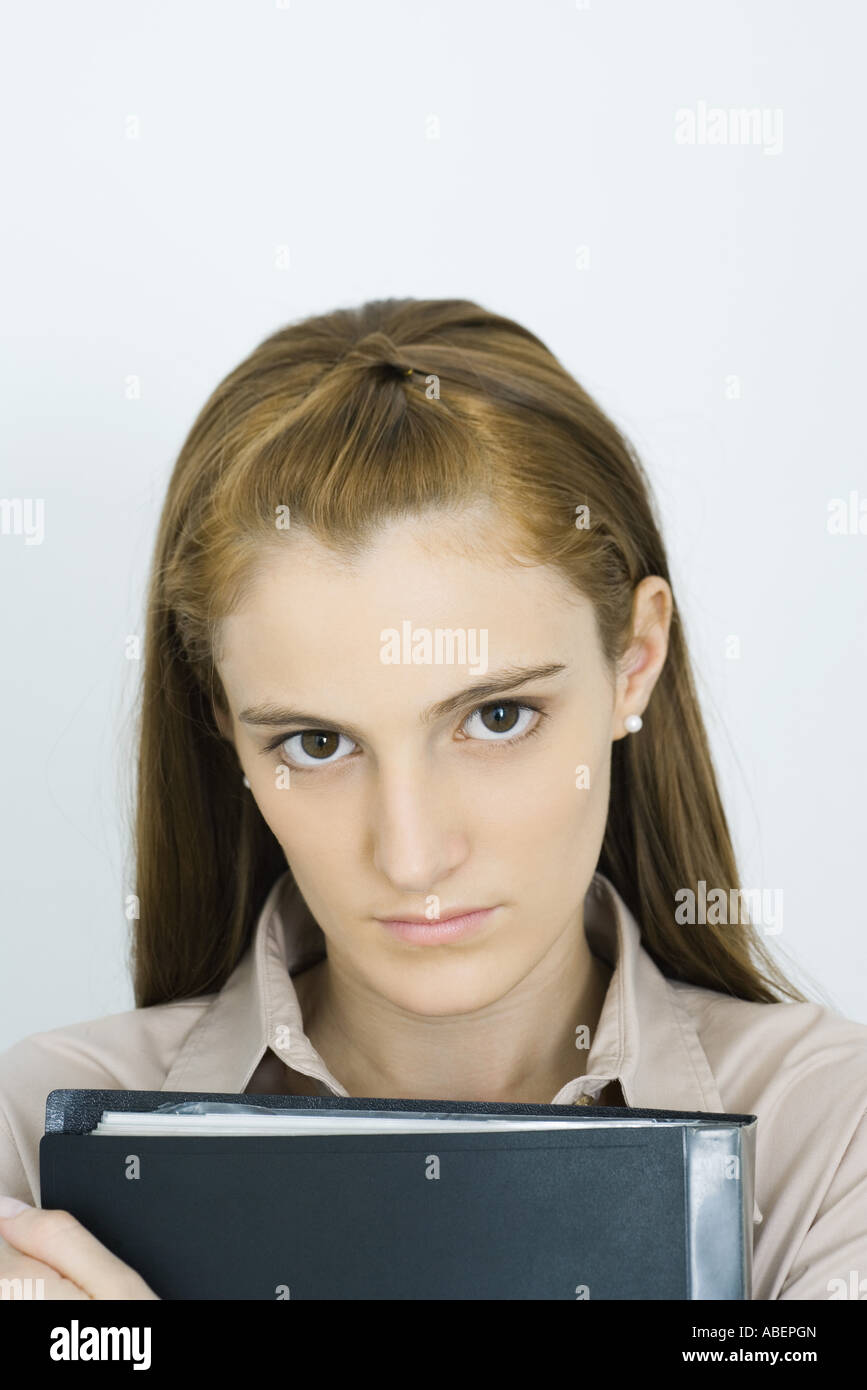 Young woman, holding binder against chest, looking at camera, portrait ...