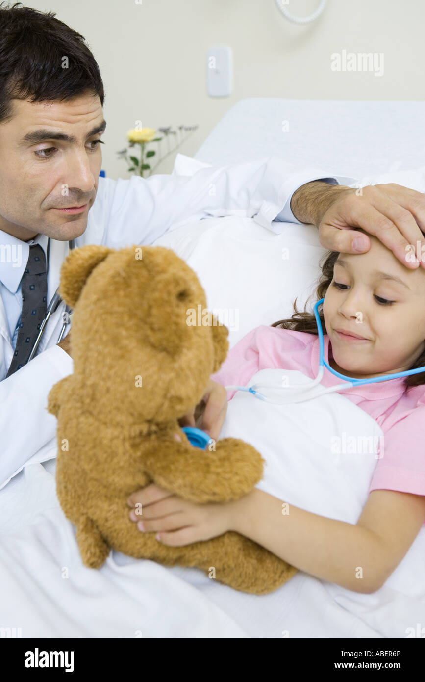 Child holding toy stethoscope to teddy bear, doctor feeling child's ...