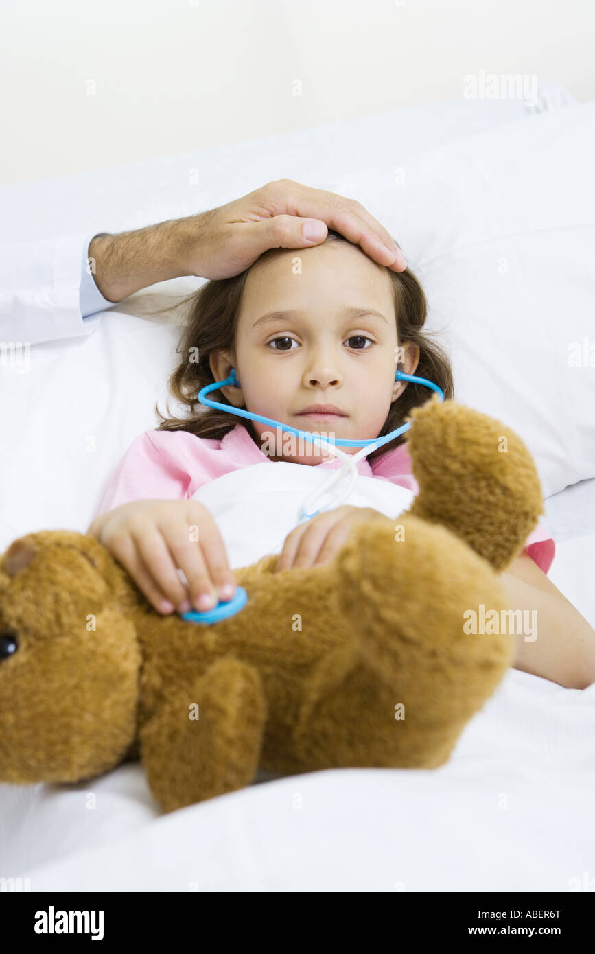 Child holding toy stethoscope to teddy bear, doctor feeling child's ...