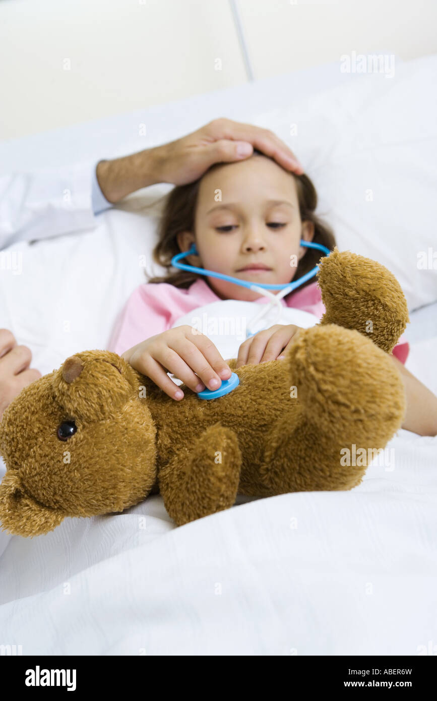 Child holding toy stethoscope to teddy bear, doctor feeling child's ...
