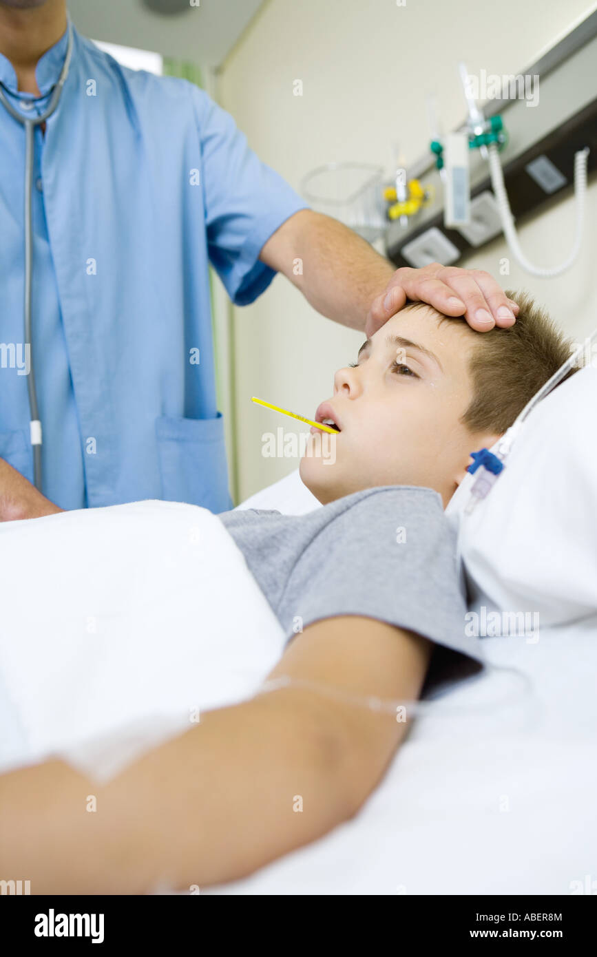 Boy lying in hospital bed, doctor taking temperature and feeling ...