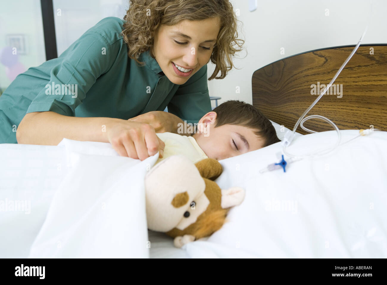 Boy lying in hospital bed asleep, nurse covering boy with blanket Stock ...