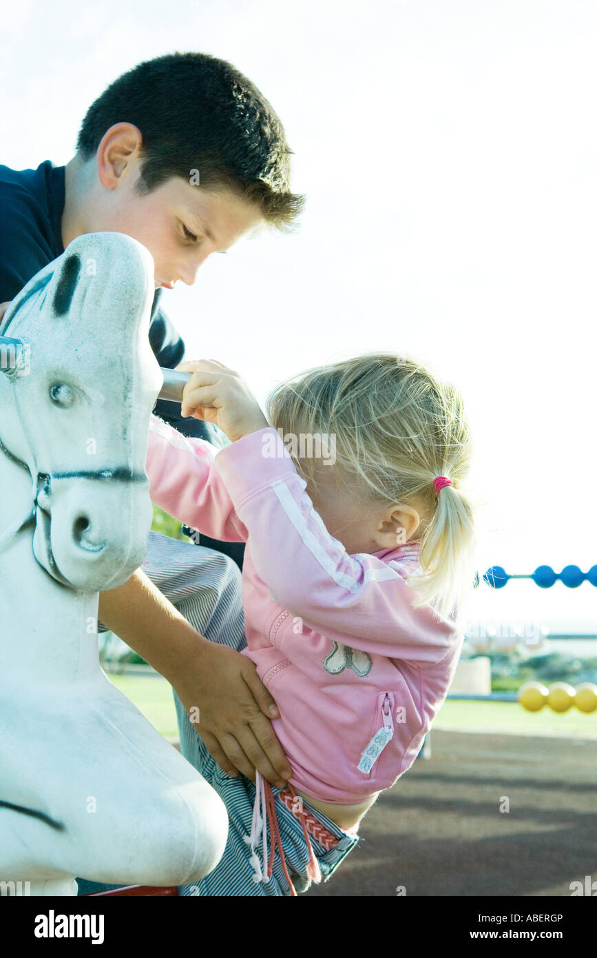 Boy helping girl onto rocking horse Stock Photo - Alamy