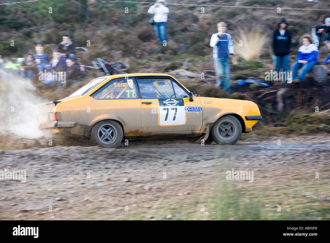 Yellow Ford Escort RS2000 rally car 77 driving on gravel stones and mud ...