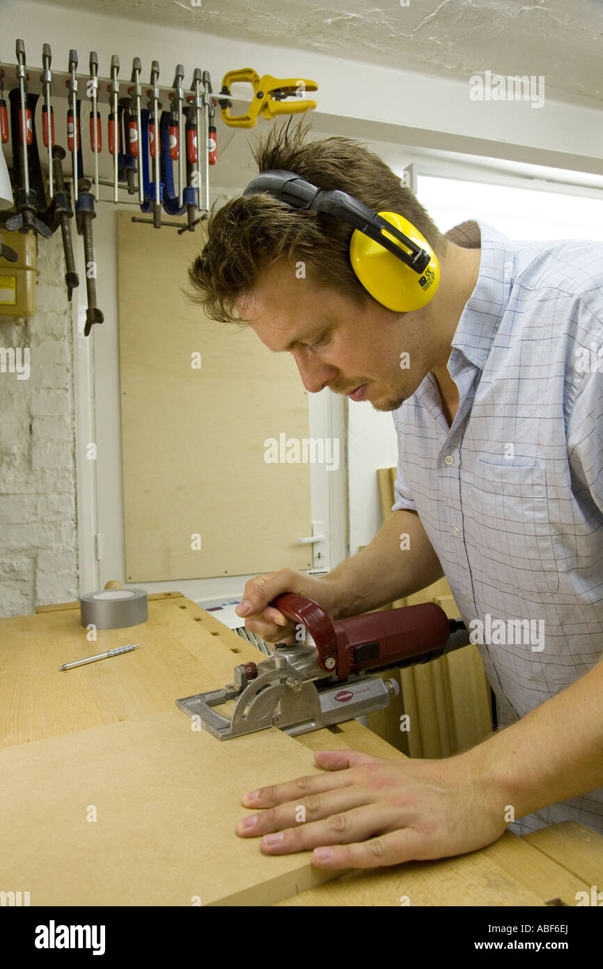 A craftsman uses a biscuit jointer to cut joints in a piece of ...