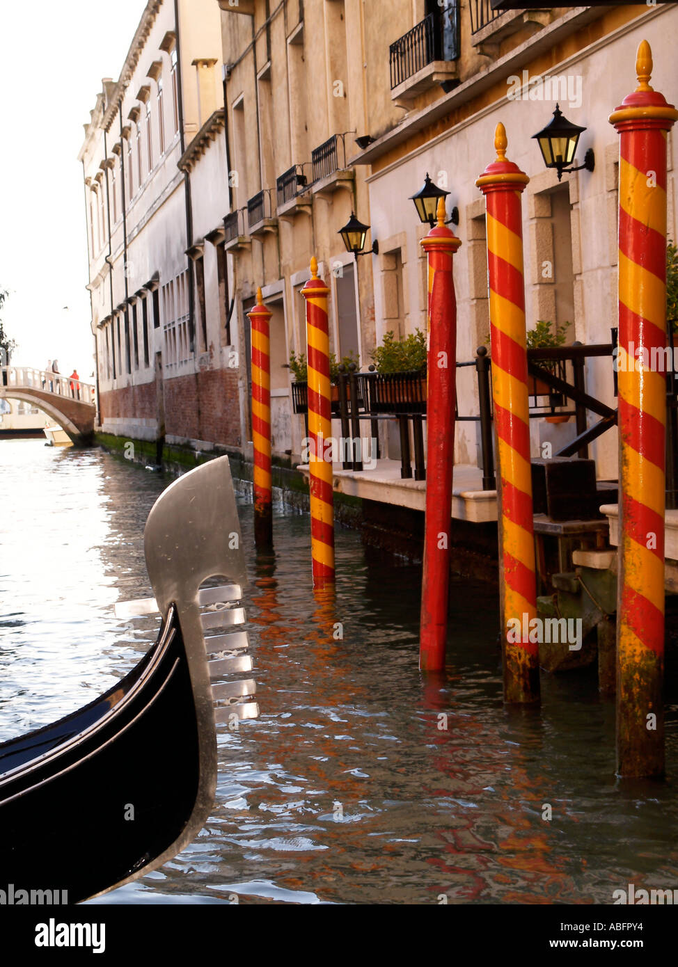 bow of gondola and red and yellow striped poles in water in Venice ...