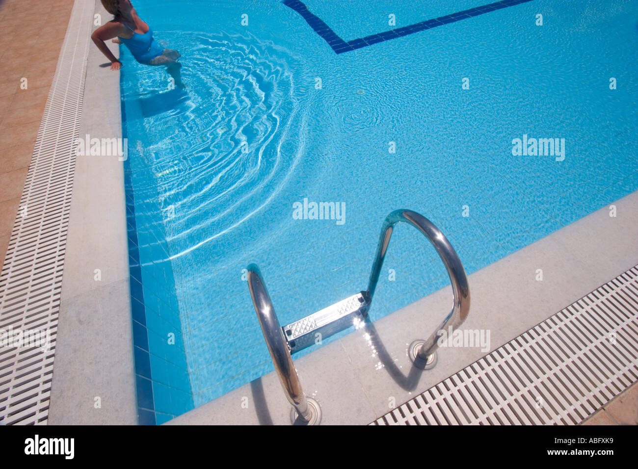 swimmer getting into swimming pool with ripples and pool steps ladder ...