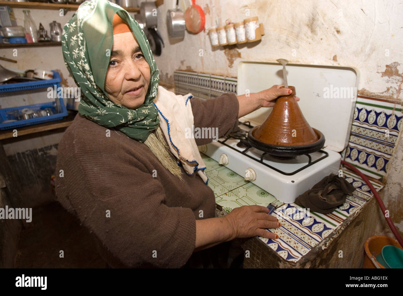 Berber woman cooks using tagine vessel in mud brick house kitchen old ...