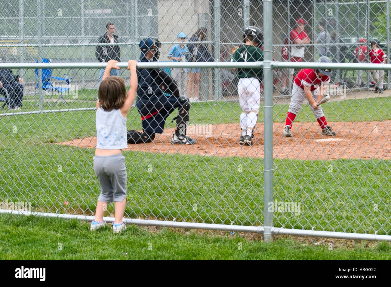 Young girl watching a Little League baseball game through the fence ...