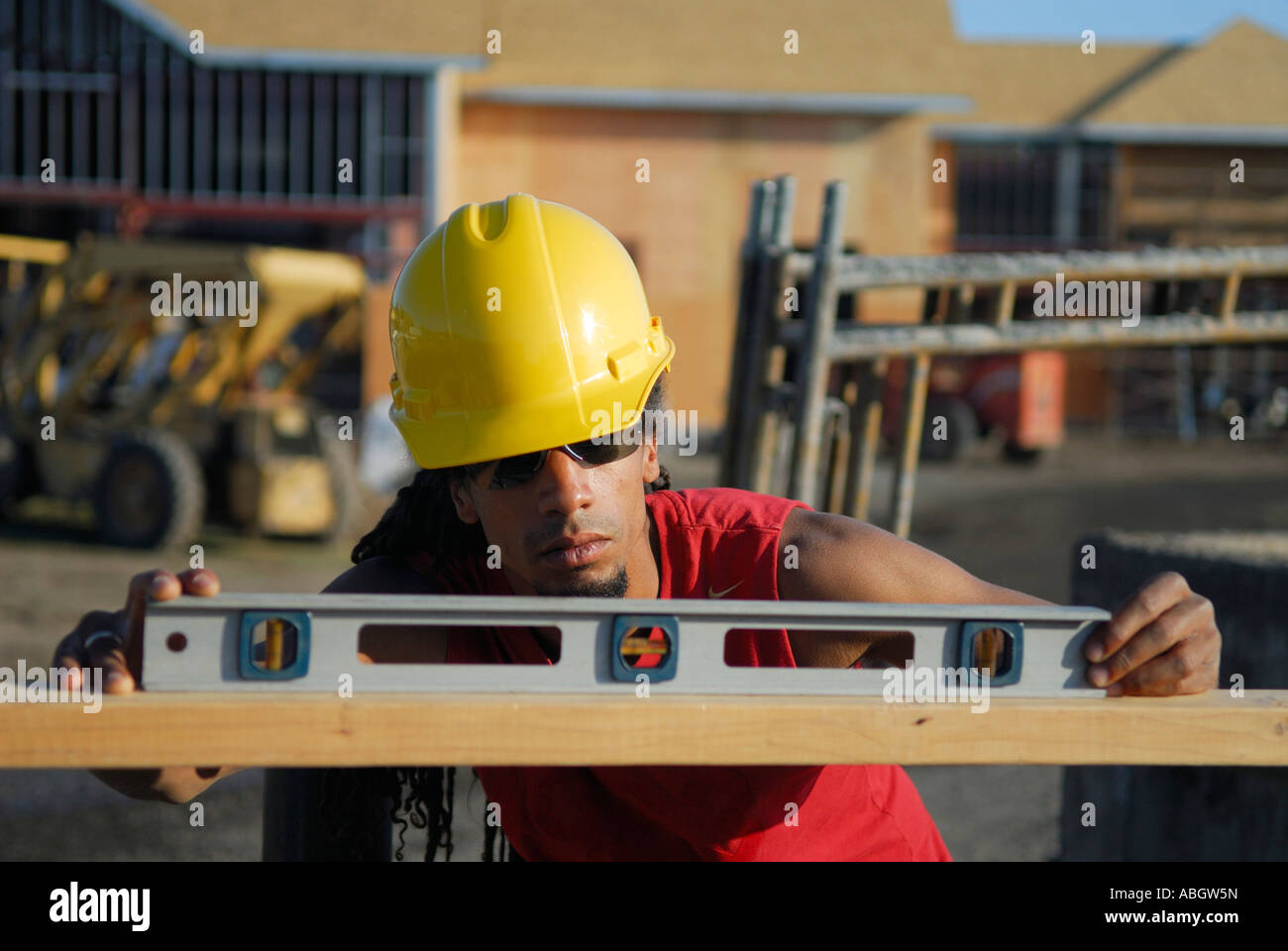 Black construction worker in hard hat checking the level of a plank of ...