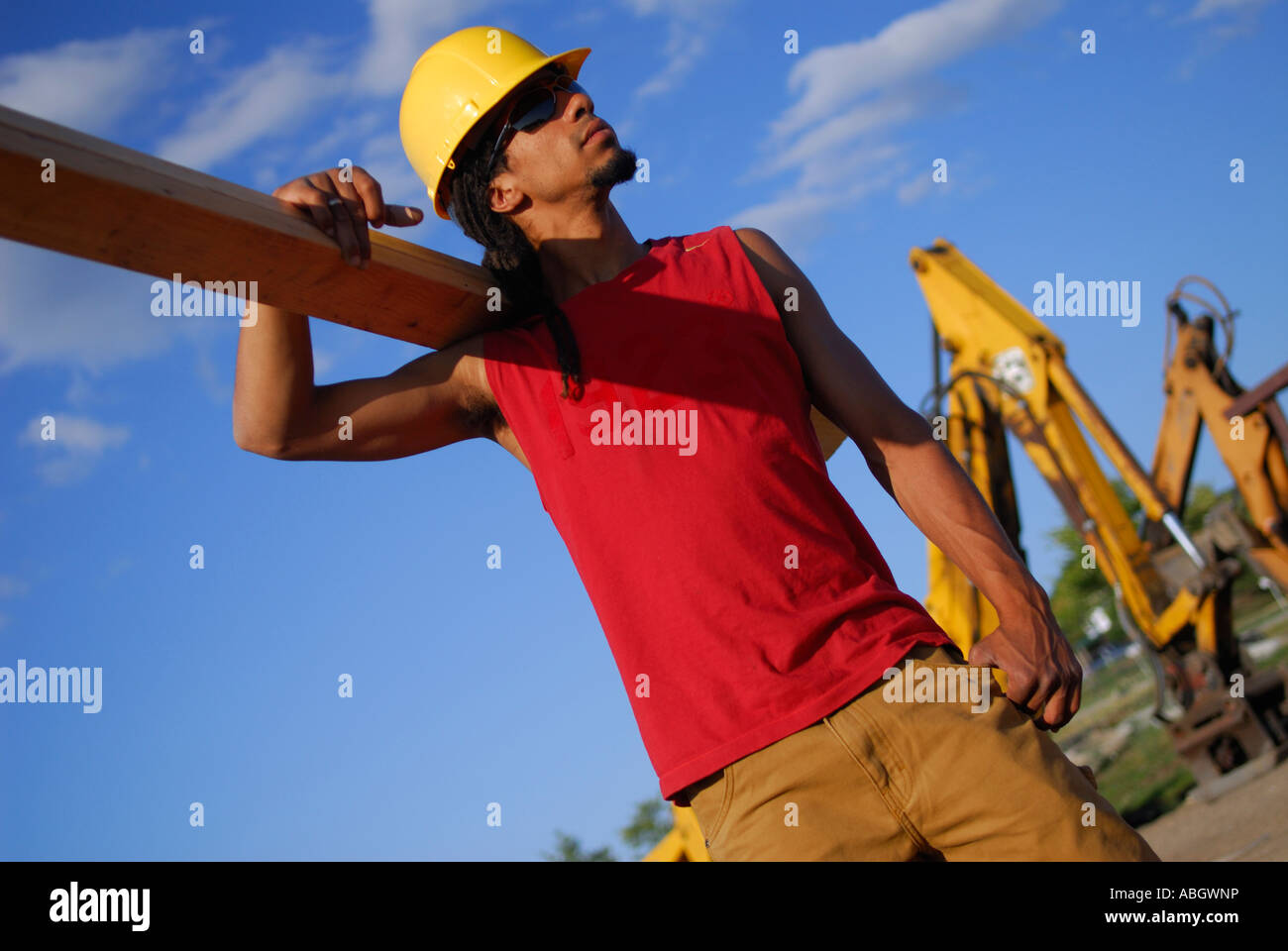 Young black man with hard hat carrying lumber on shoulder at a ...