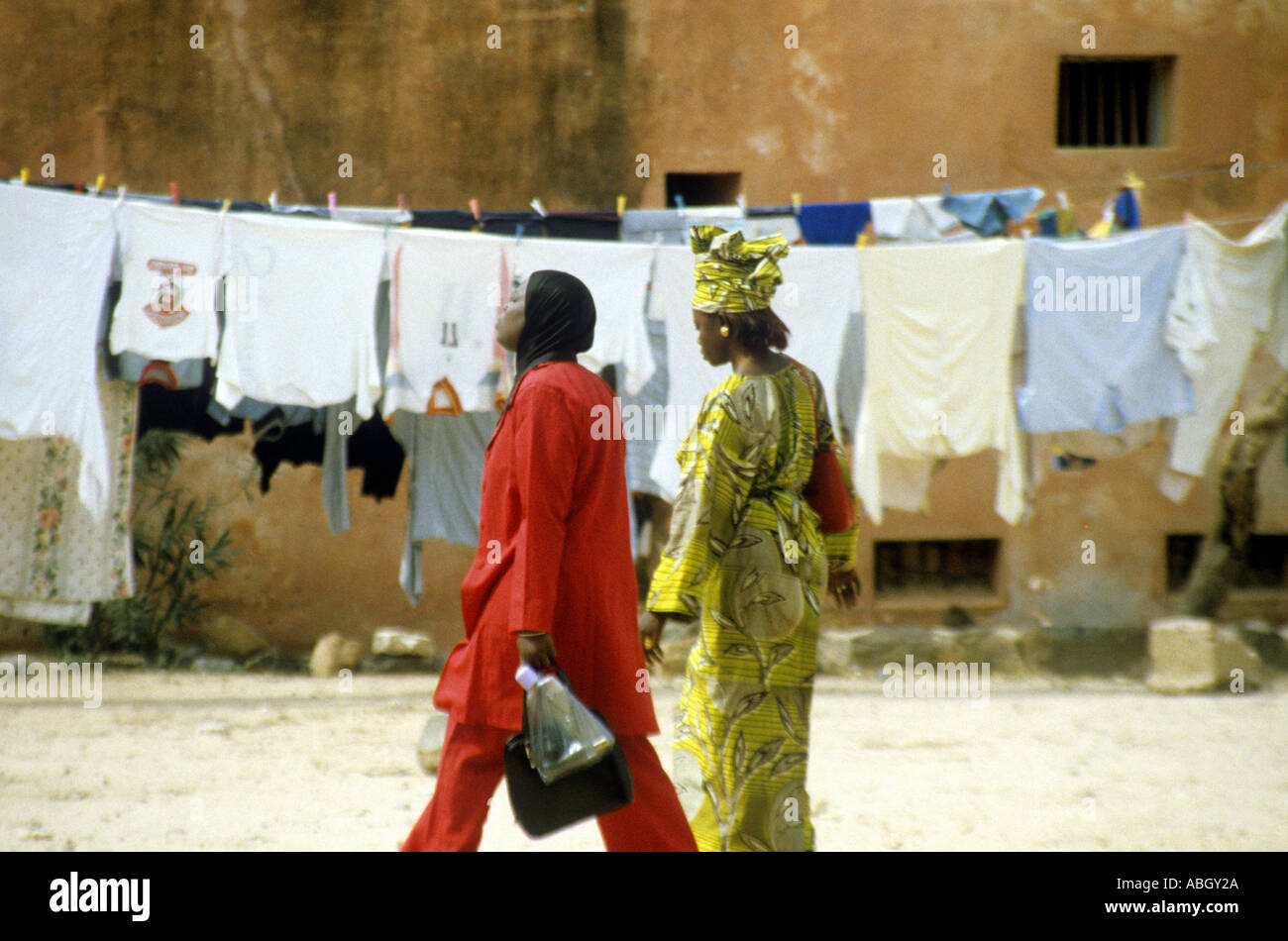 Women in traditional African Muslim dress walk past washing lines with ...