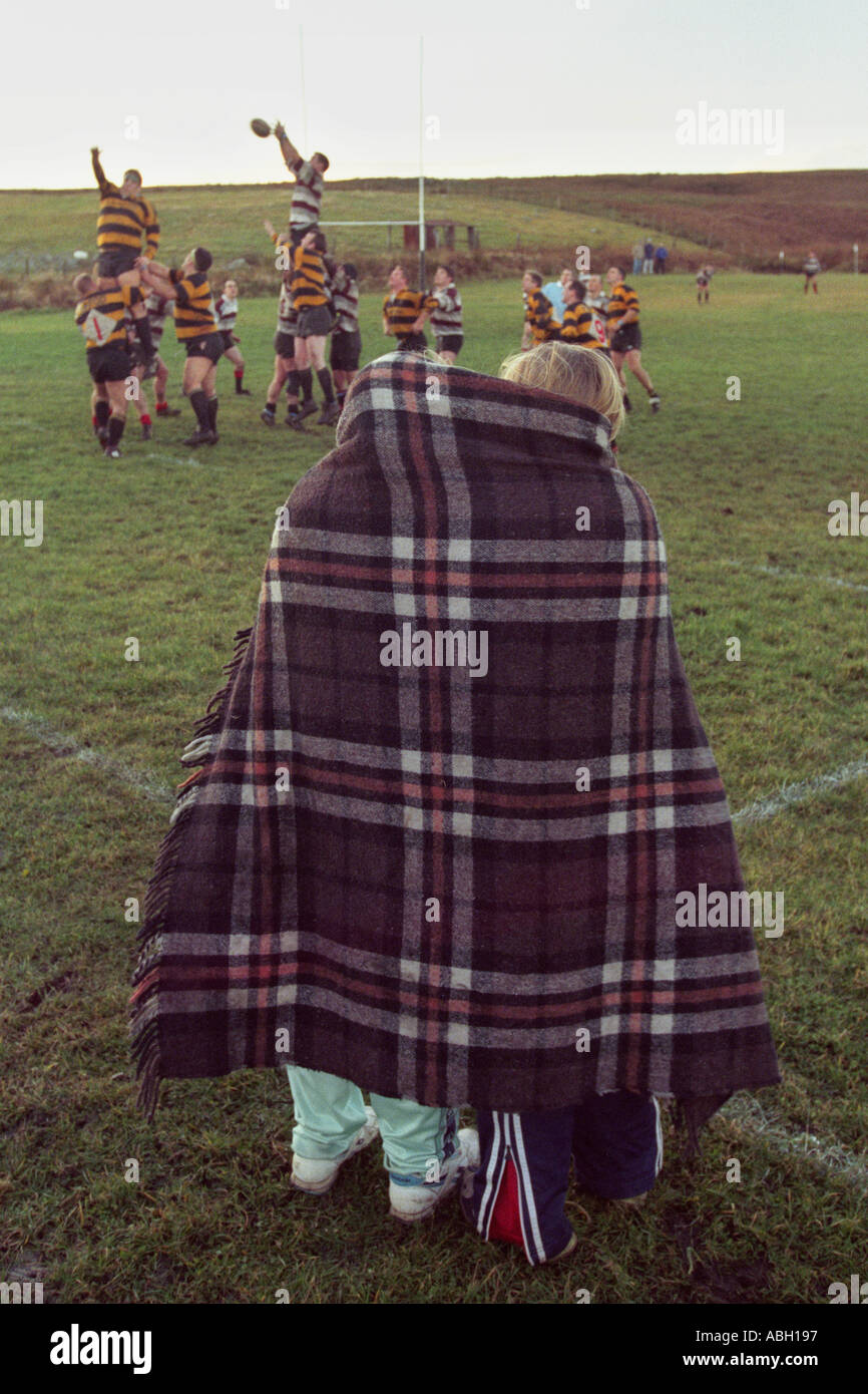 Two young girls huddle in a Welsh shawl watching a rugby union match at ...