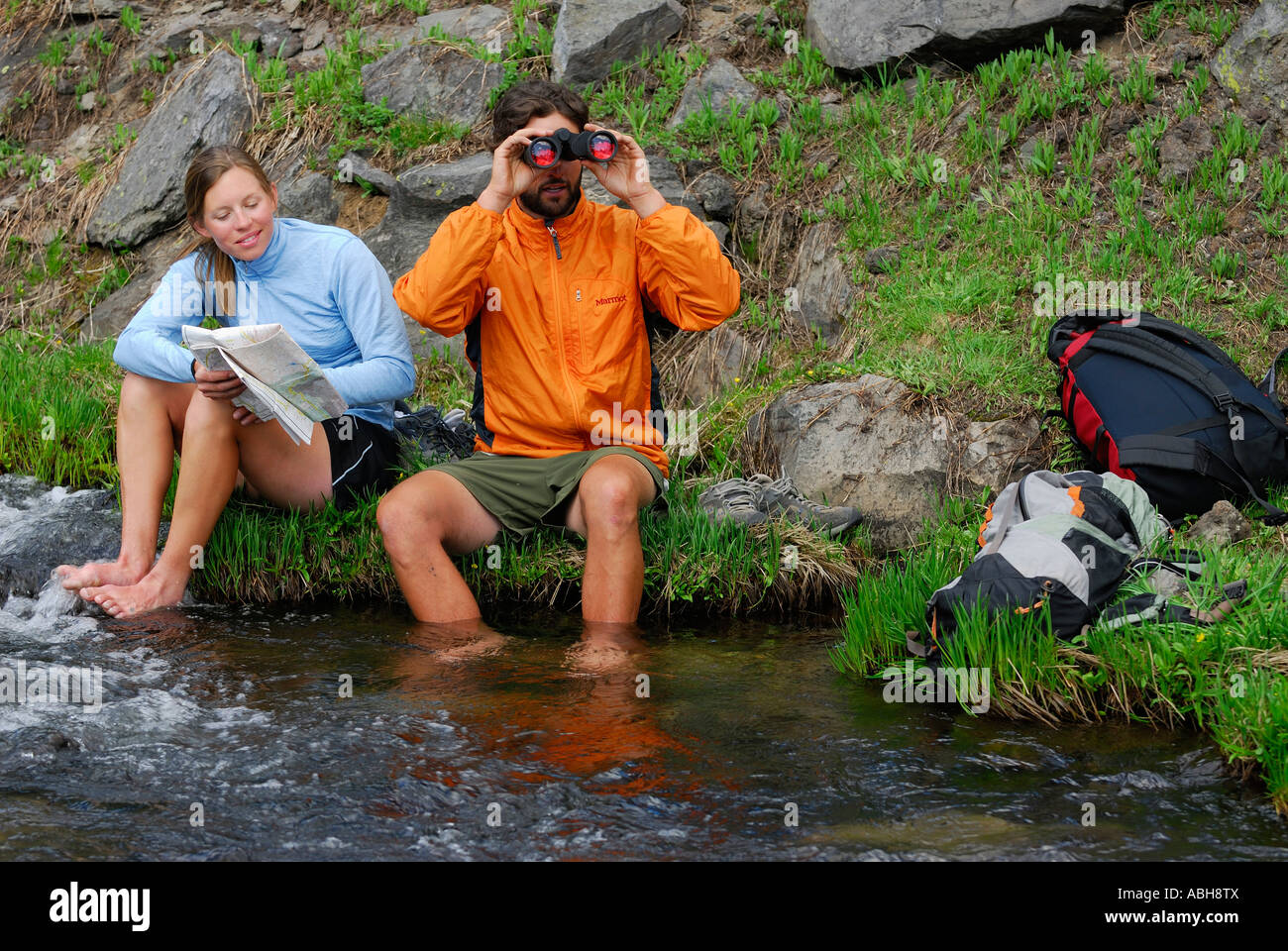 Young couple of hikers with feet in a stream checking directions with ...