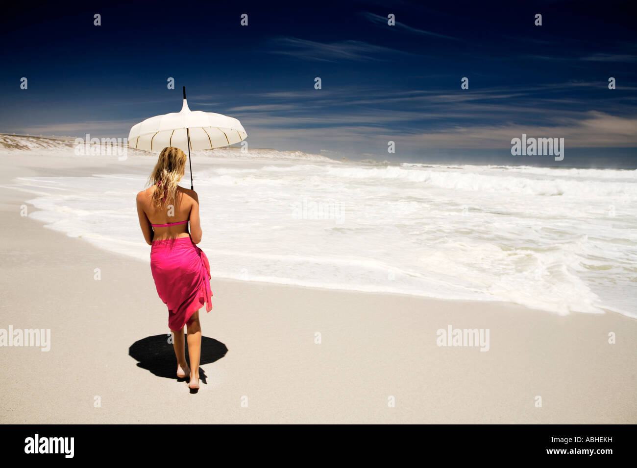 Young woman in bikini and pareo with parasol on the beach, rear view ...