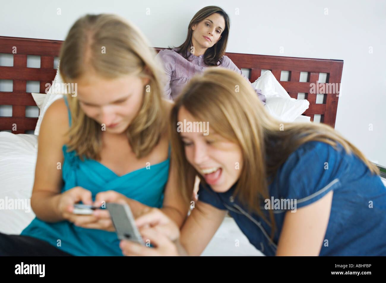 2 smiling teenage girls using mobile phones, woman in background Stock ...