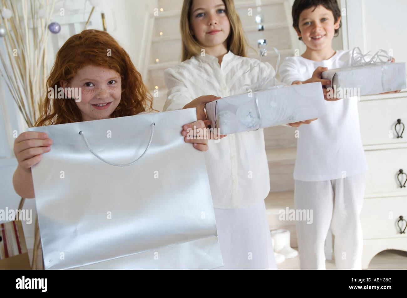 Three children offering Christmas presents, indoors Stock Photo - Alamy
