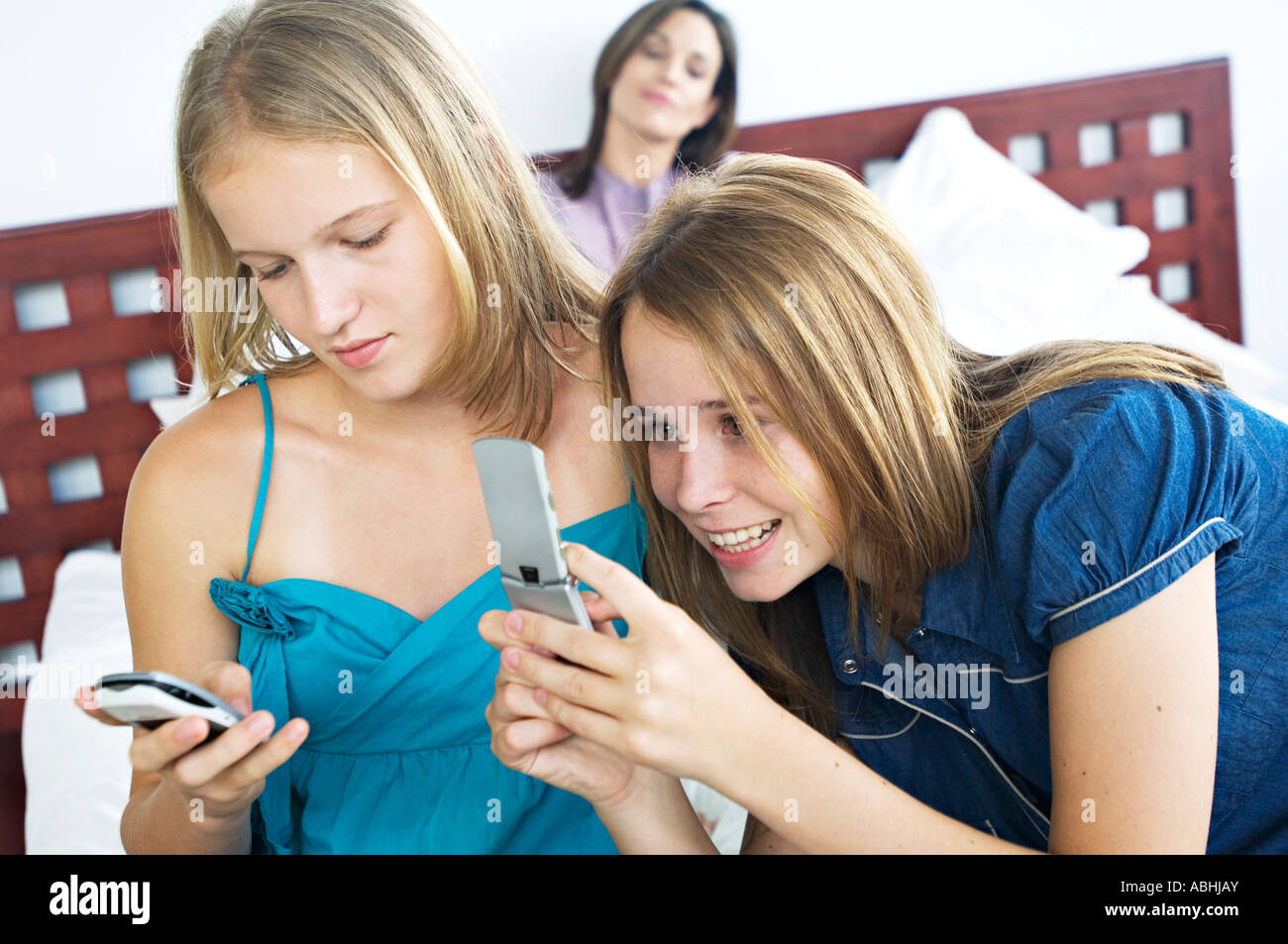 2 smiling teenage girls using mobile phones, woman in background Stock ...