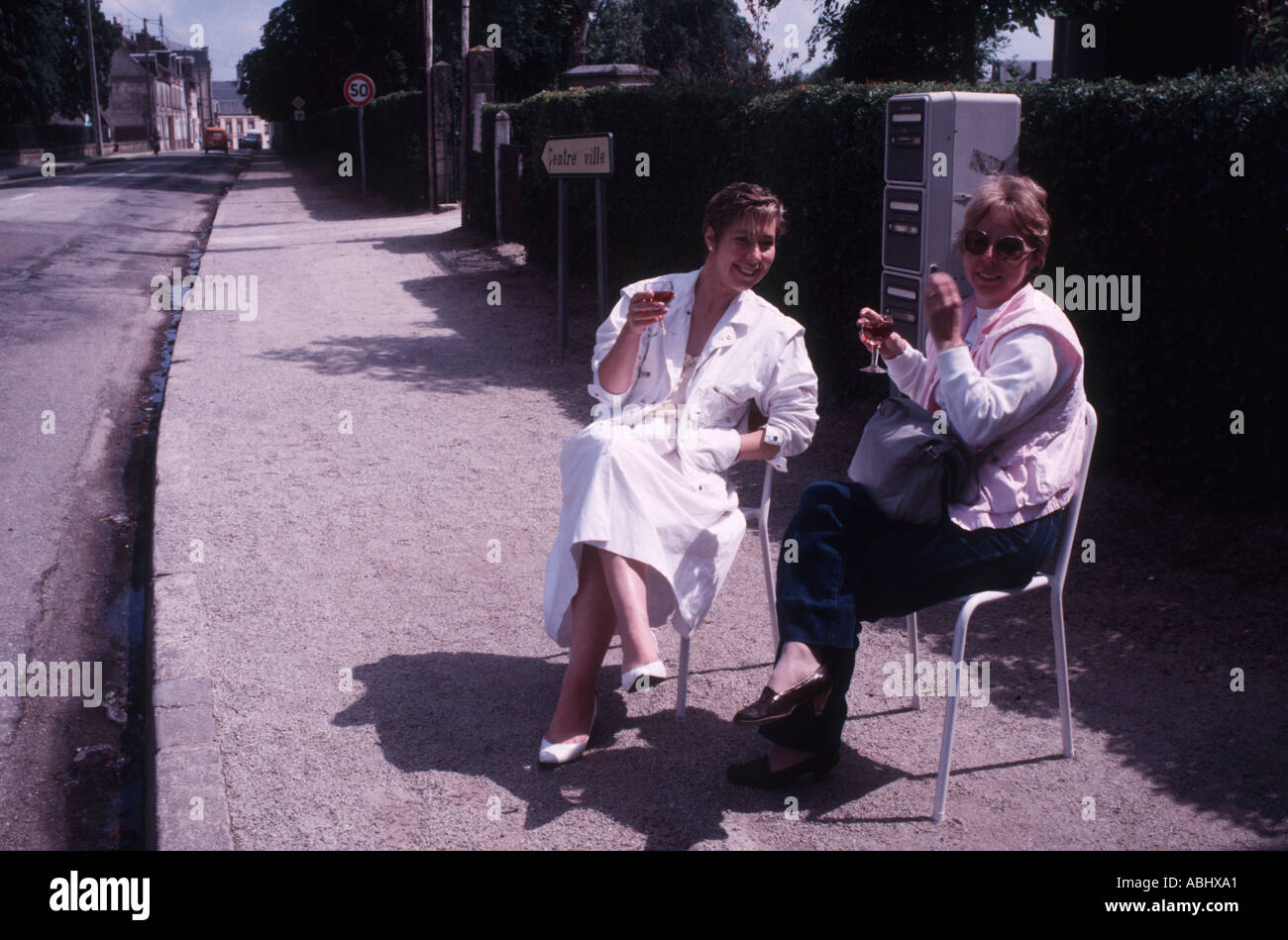France two women sitting at the roadside in a town holding glasses of ...