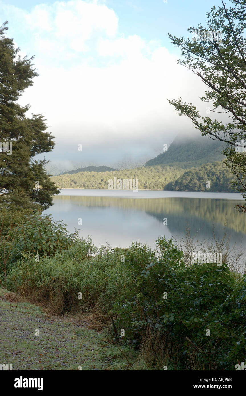 View through the trees of a lake and mountain with low cloud Stock ...