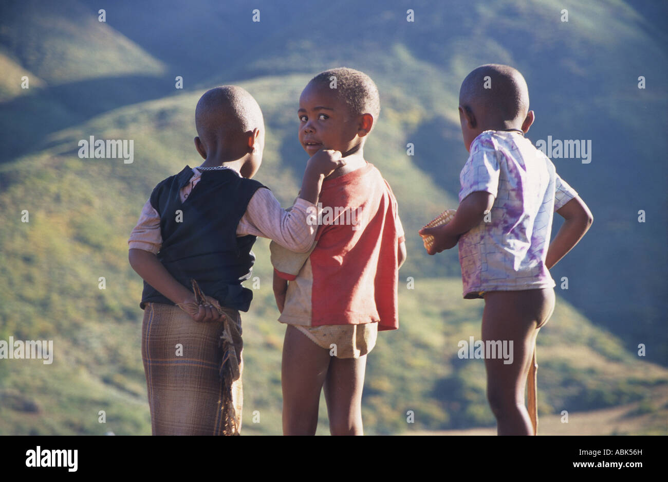 Three Afrian children stand in the mountainous scenery of Lesotho ...