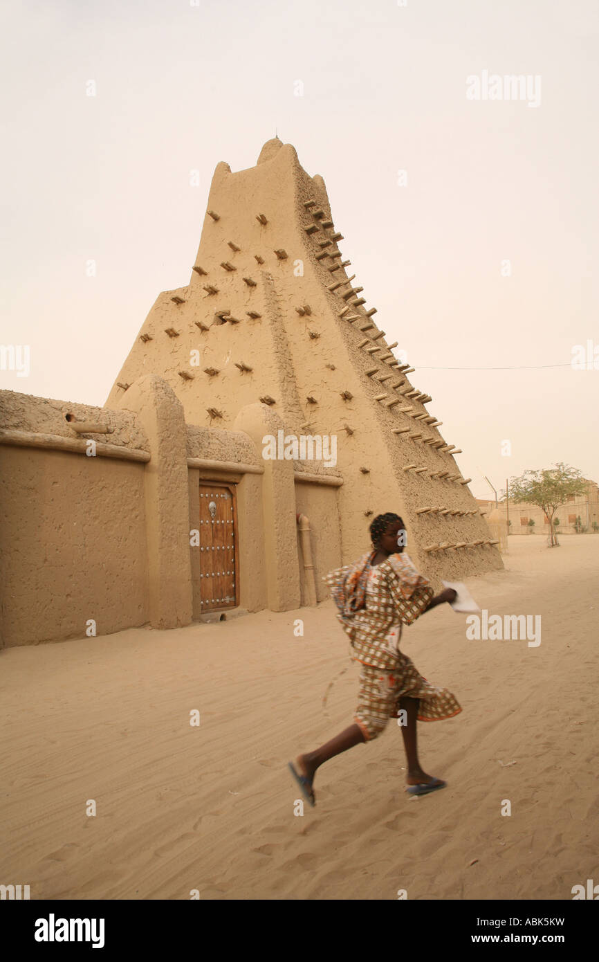 Girl running past traditional mud mosque, Timbuktu, Sahara desert, Mali ...