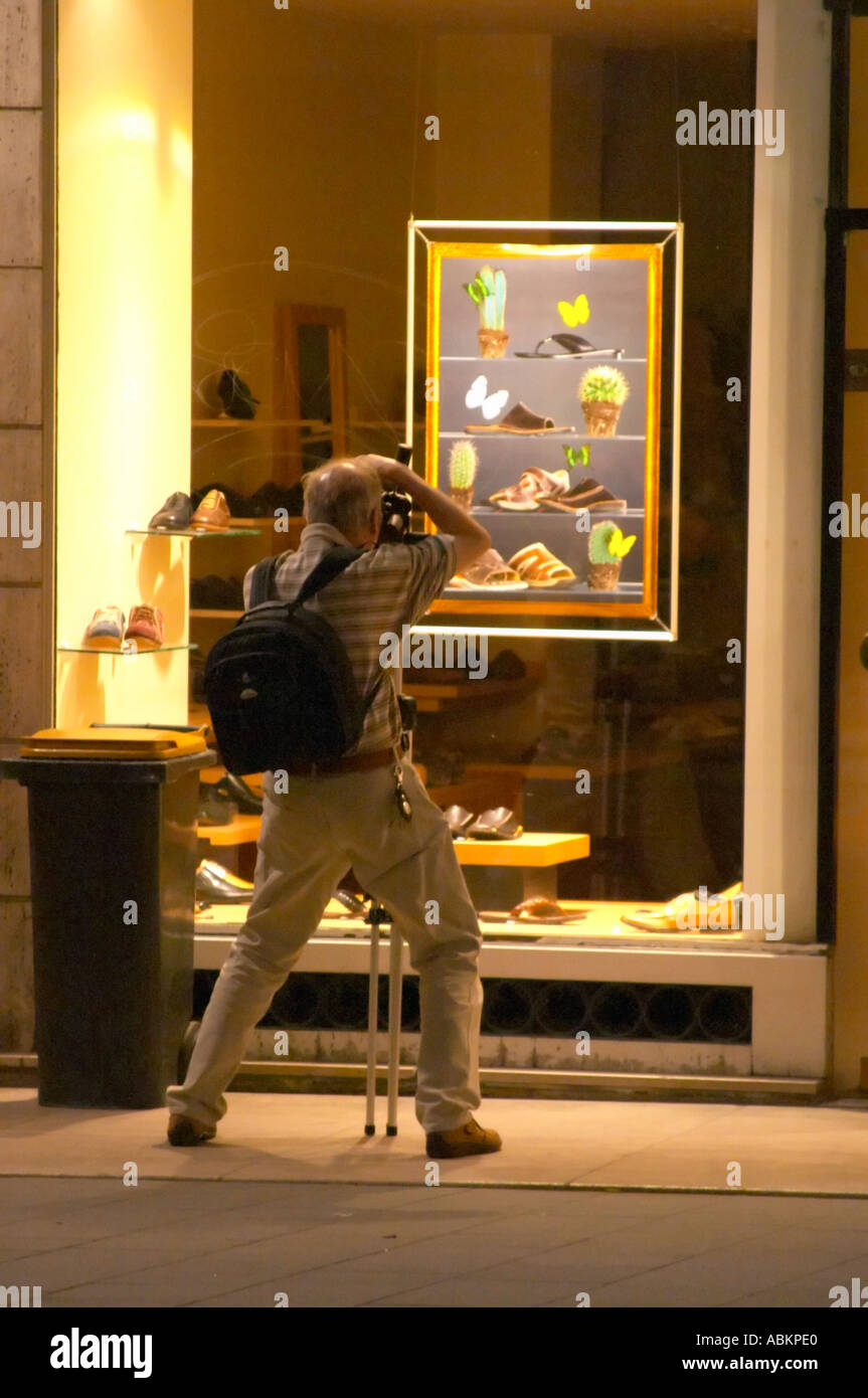 A photographer taking a picture at night of a shoe shop window display ...