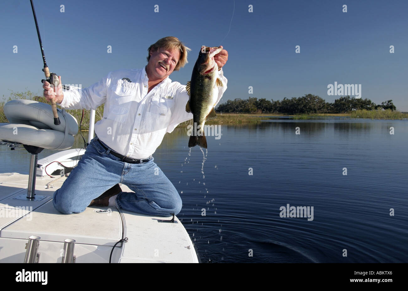 Photo of middle aged excited fisherman holding his catch large bass on ...