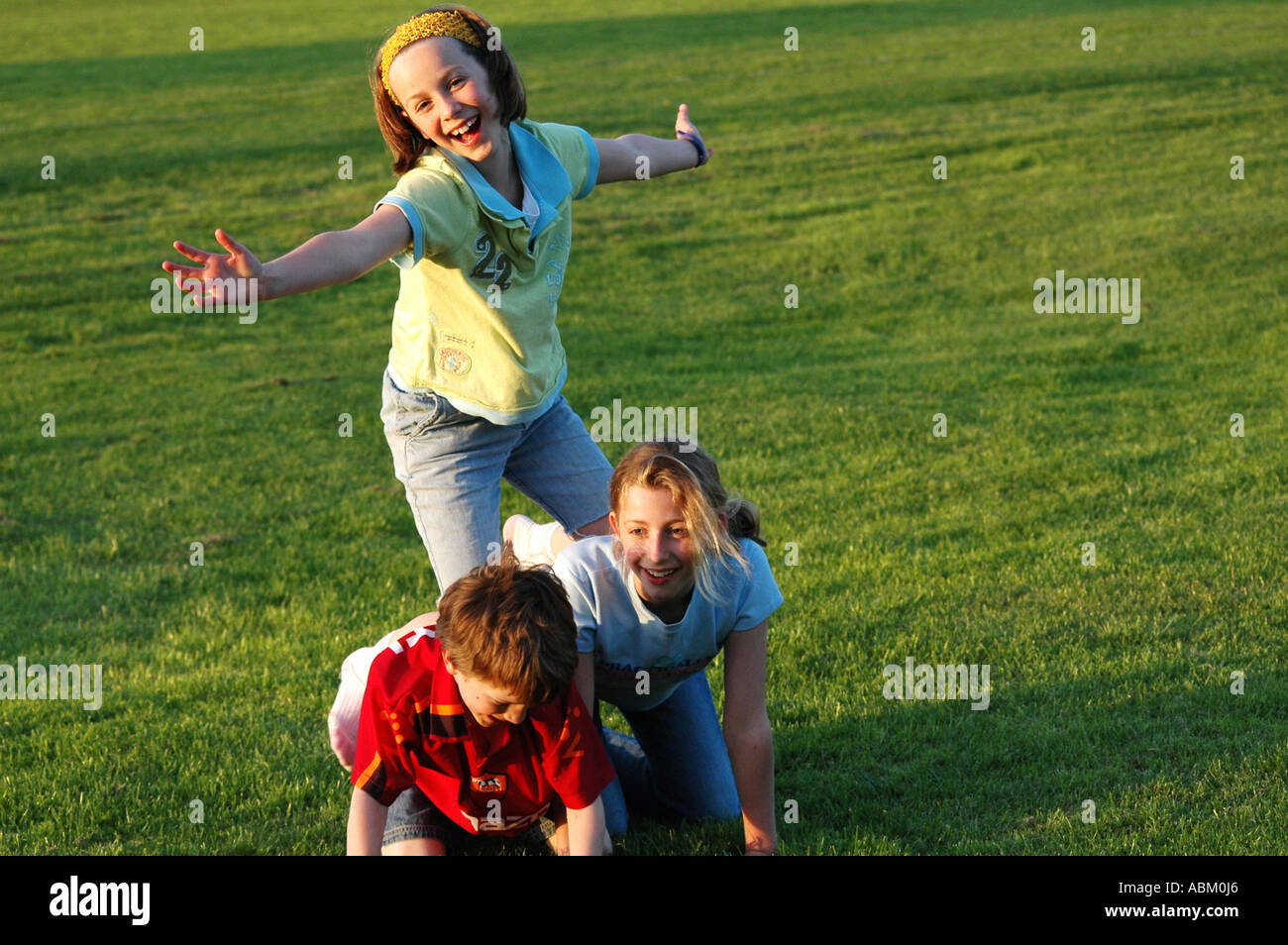portrait of three children messing about in the park and climbing on ...