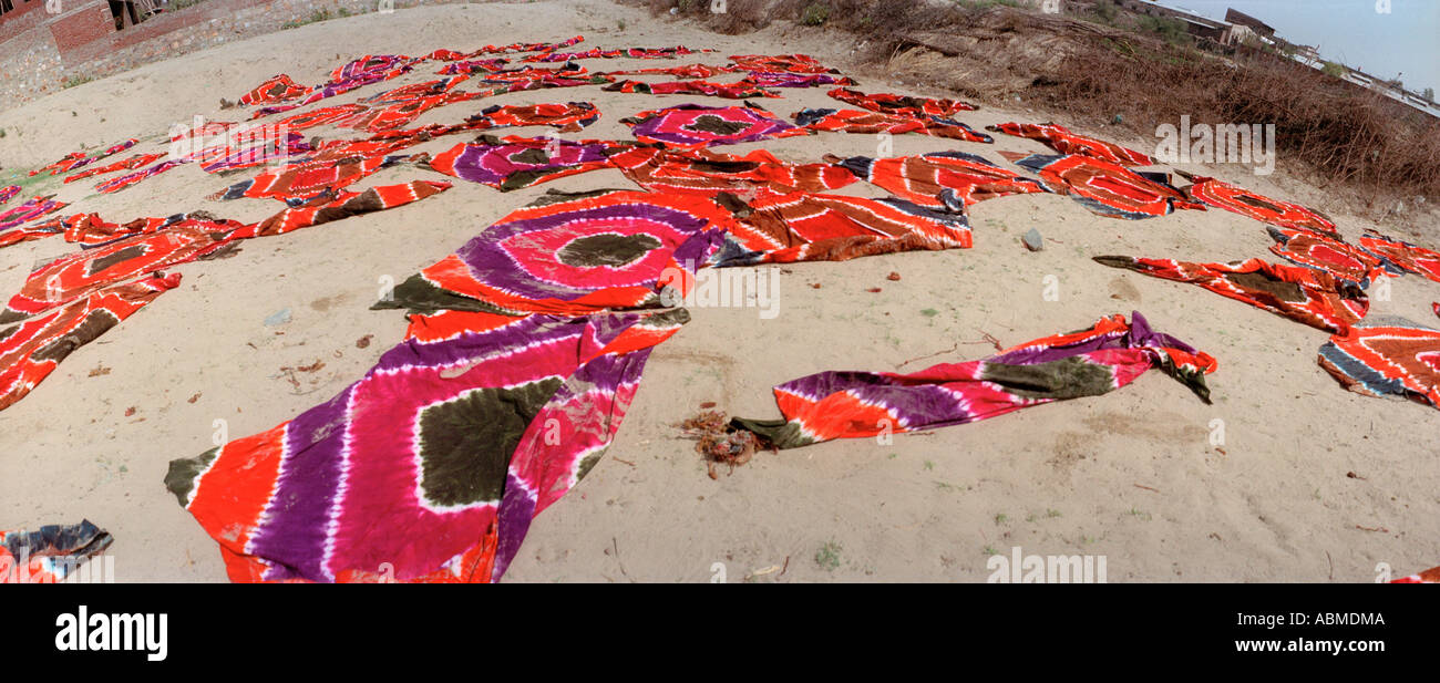 Lengths of tie dyed fabric laid out to dry on the river bank in ...